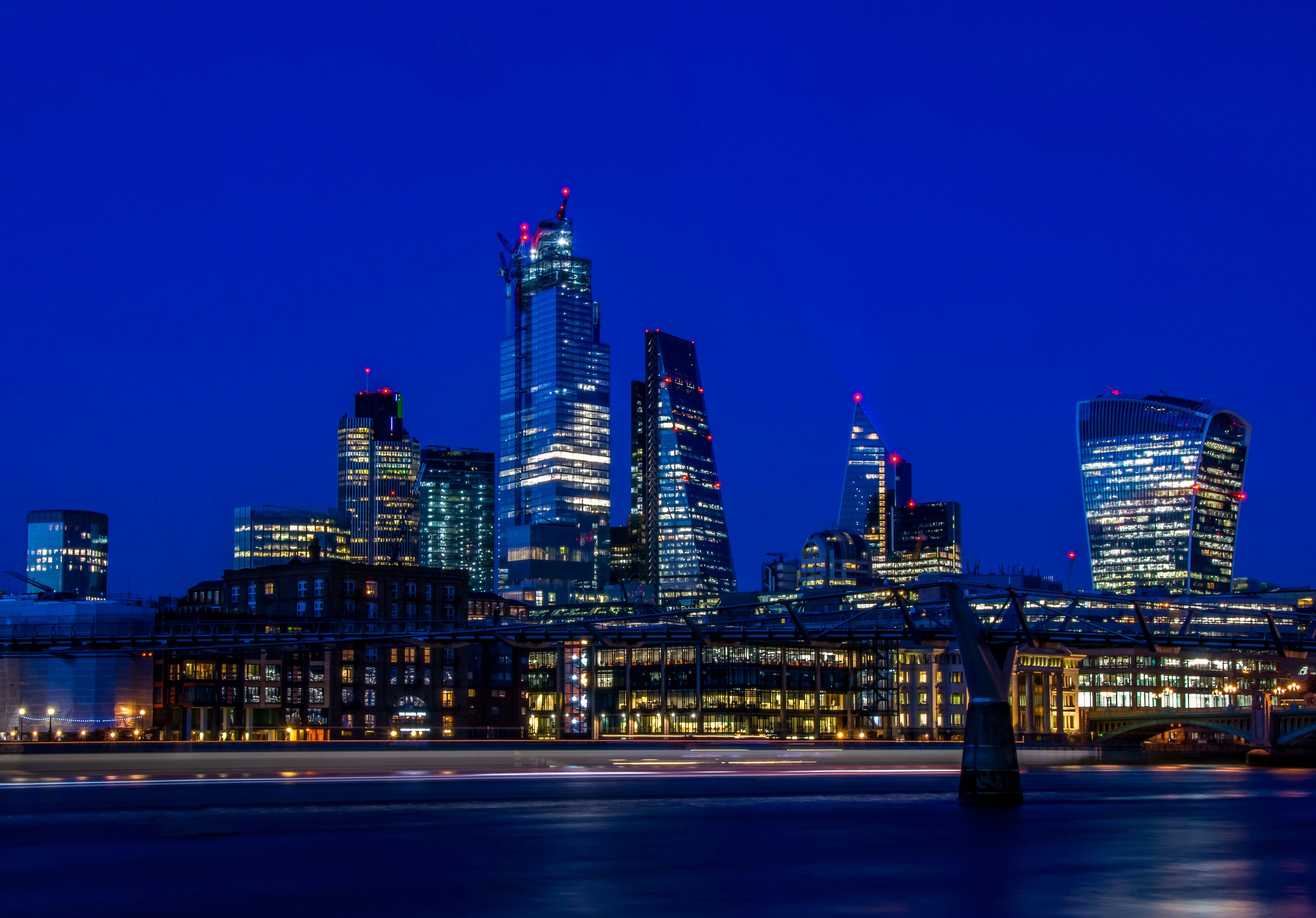 Illuminated skyline of a modern city at dusk, showcasing a blend of architectural styles and vibrant lights reflecting on the water.