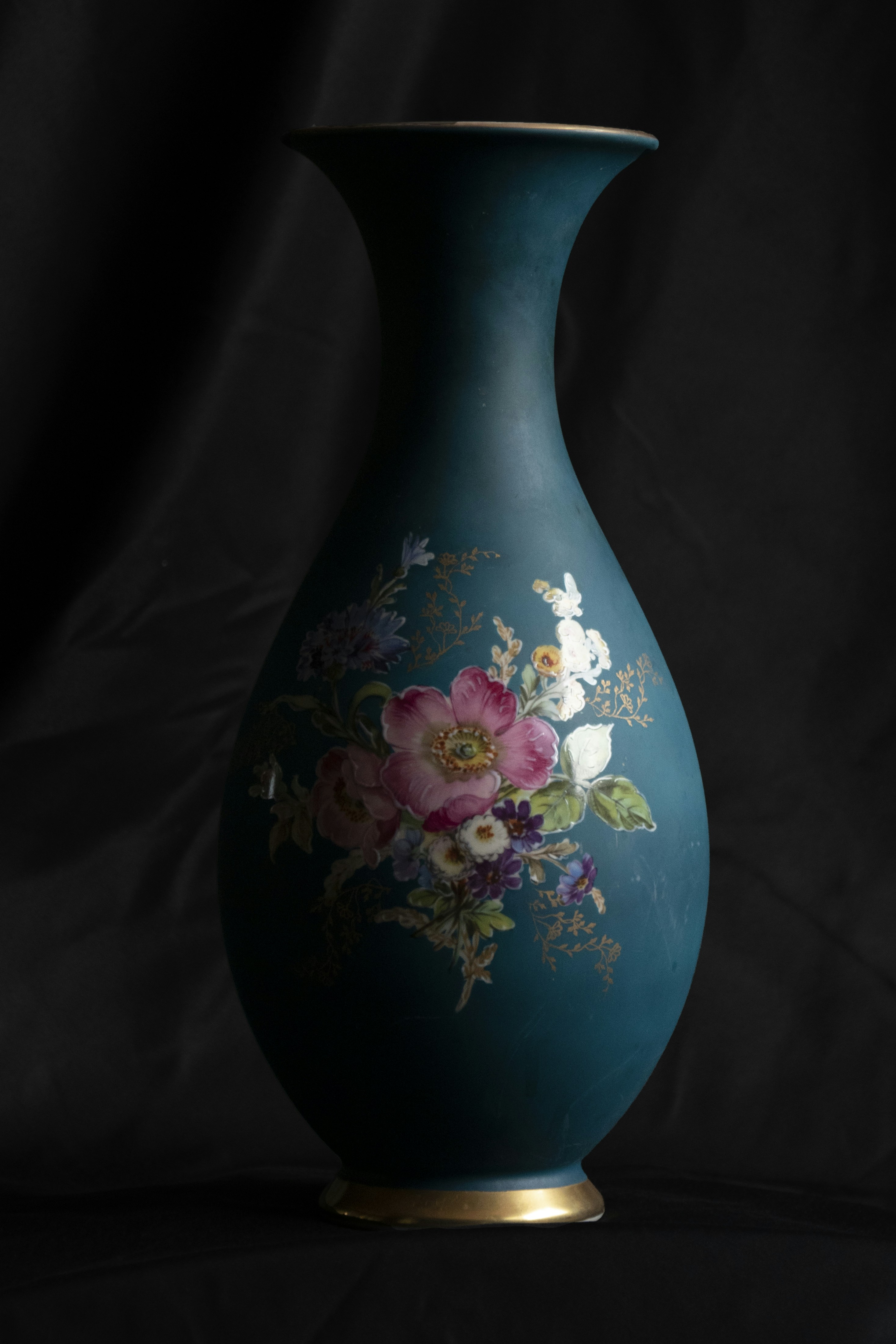 Tall blue porcelain vase adorned with delicate floral designs, set against a dark backdrop.