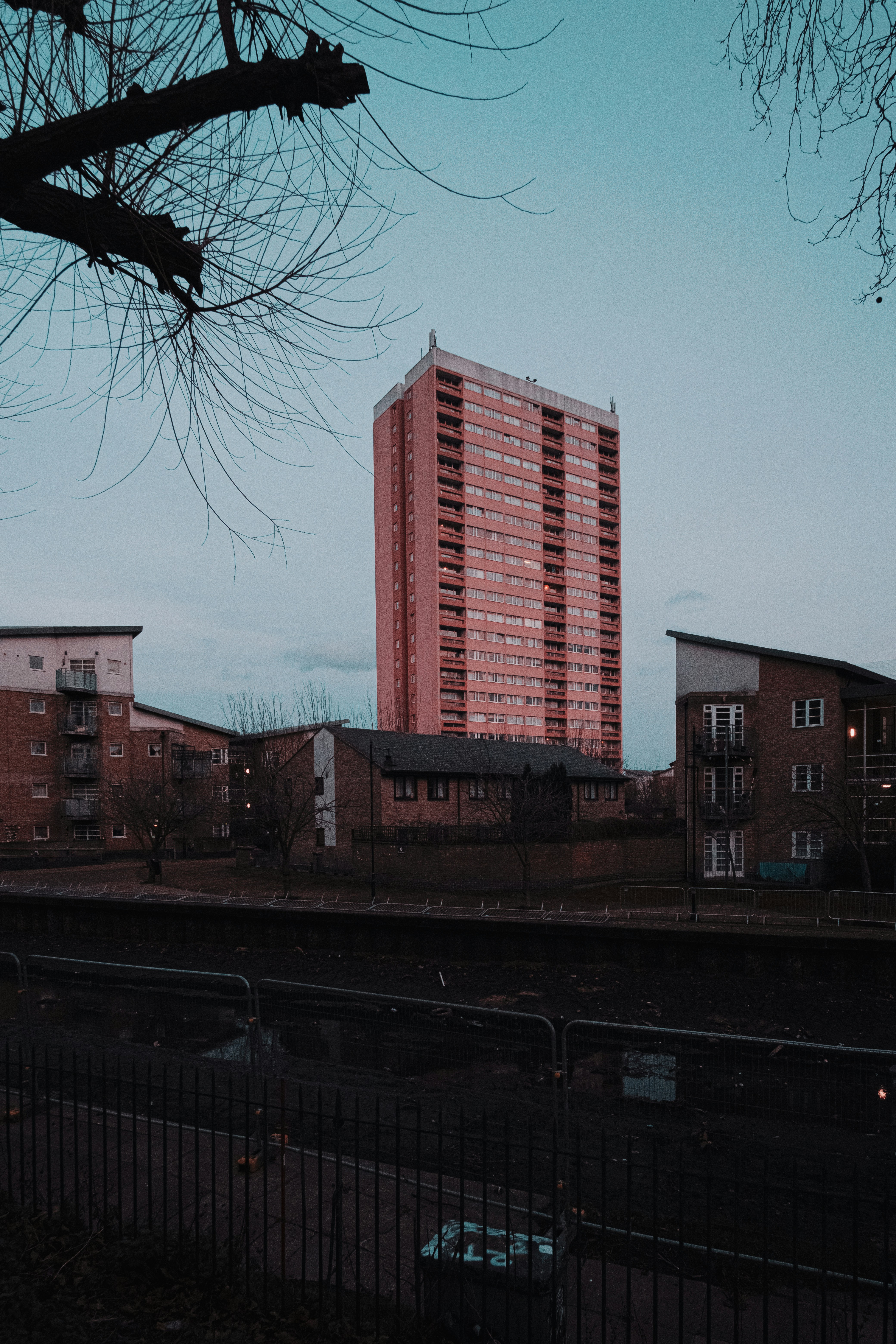 High-rise building reflecting the evening light, surrounded by residential structures and a canal. The scene captures a blend of urban architecture and nature.