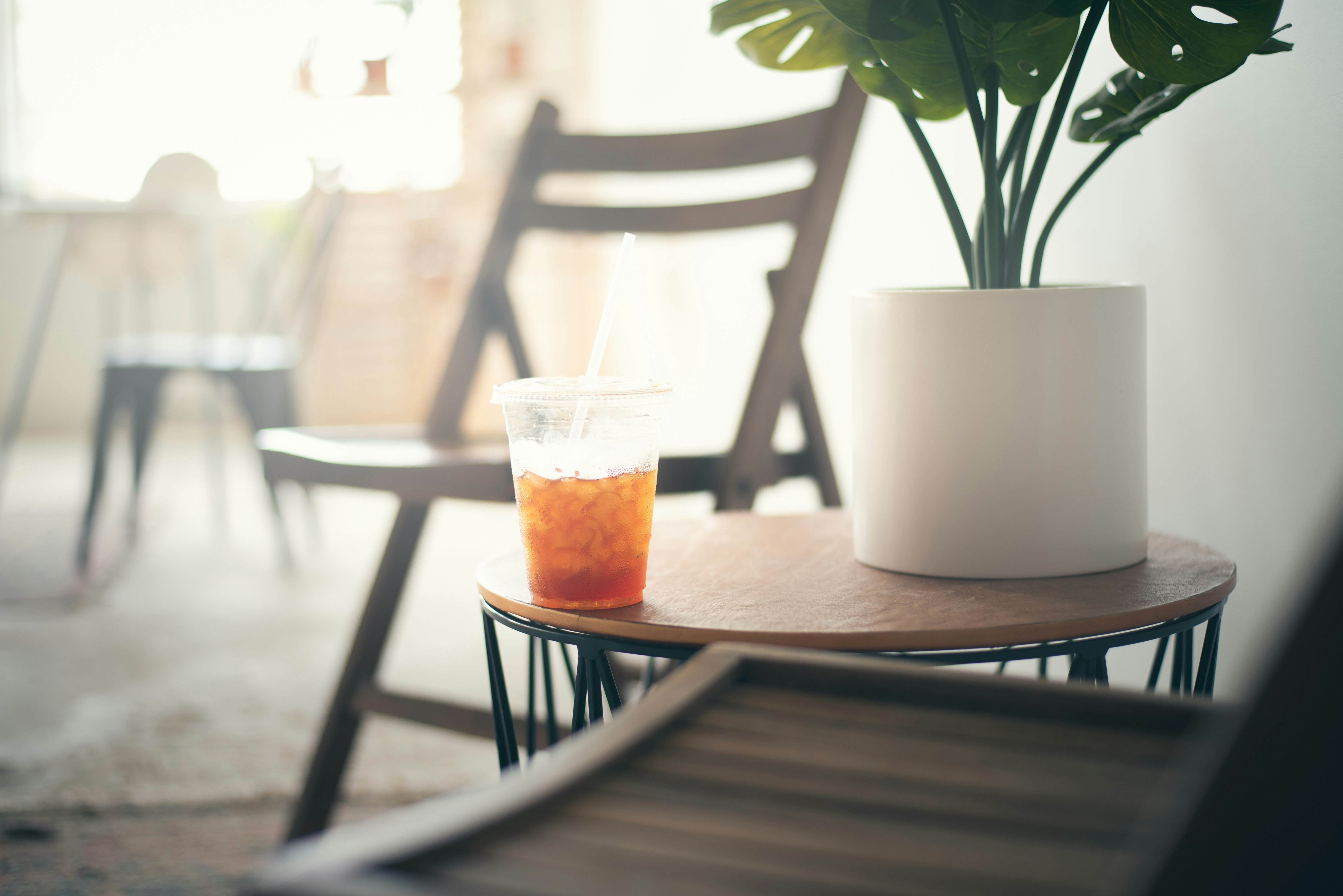 A refreshing iced drink rests on a wooden table beside a potted plant in a cozy, softly lit room.
