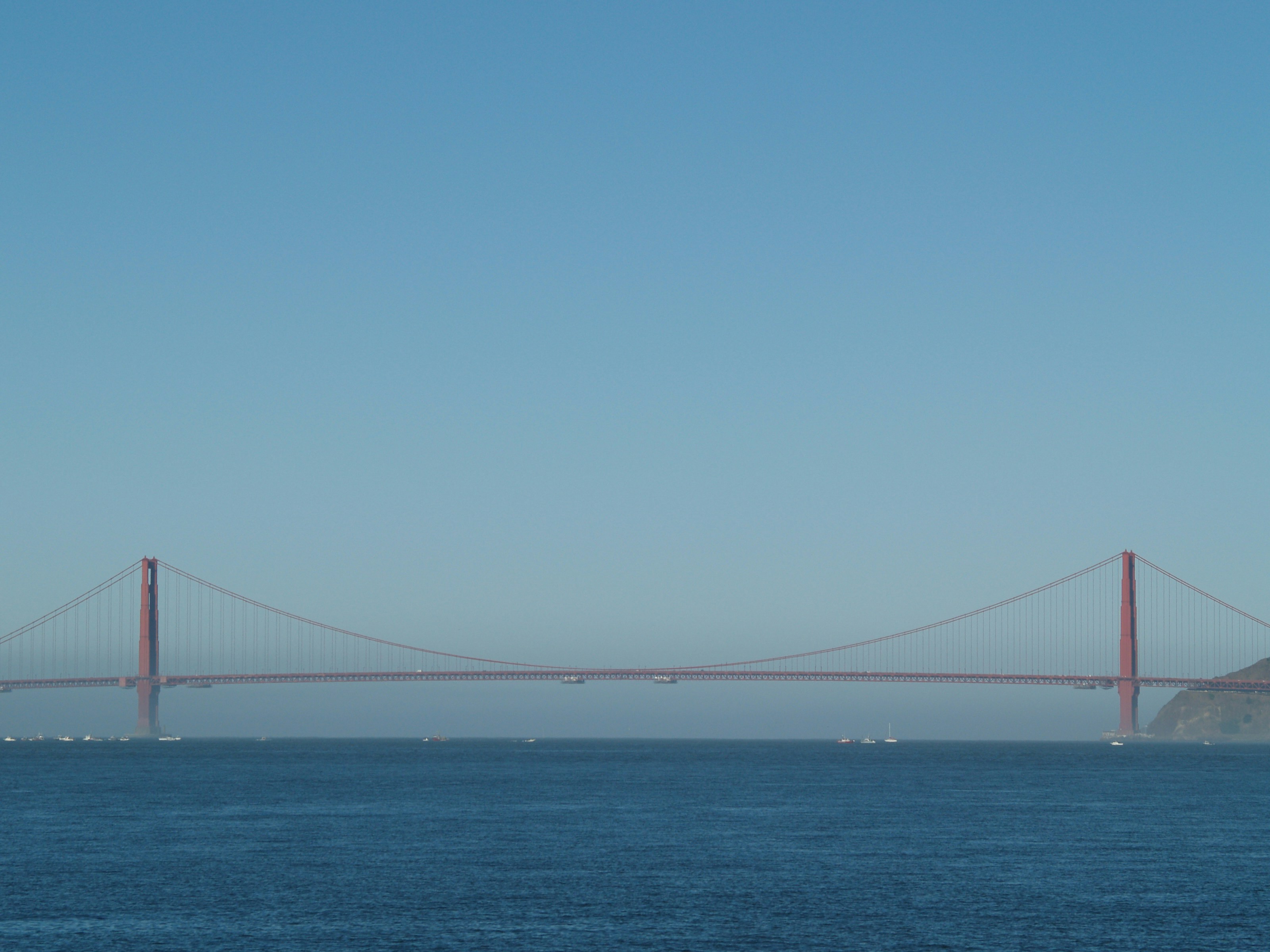 Golden Gate Bridge spanning across the bay under a clear blue sky, with boats dotting the water's surface.