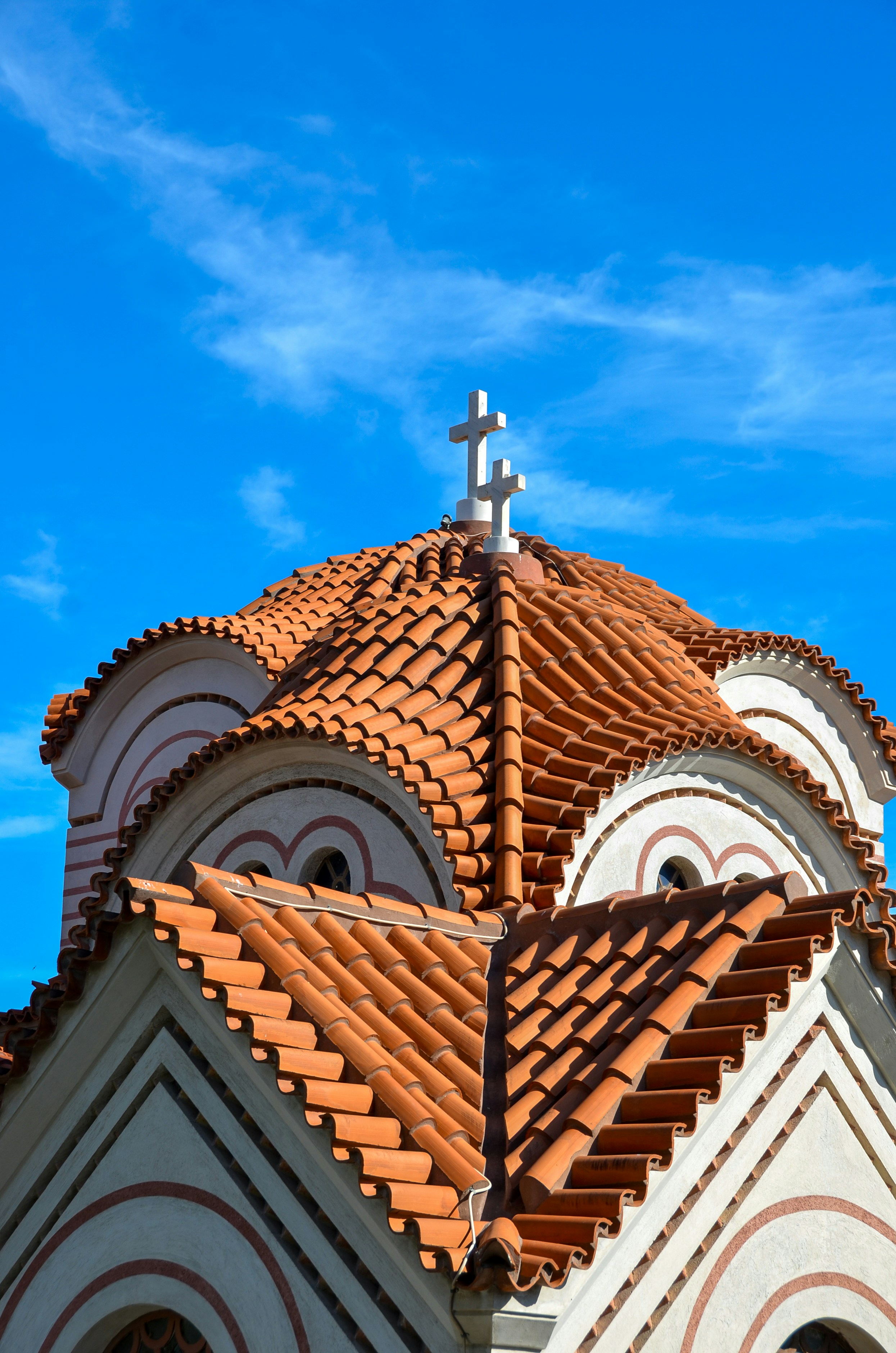 Terracotta Tapestry: Cross-Topped Roof against a Clear Azure Sky