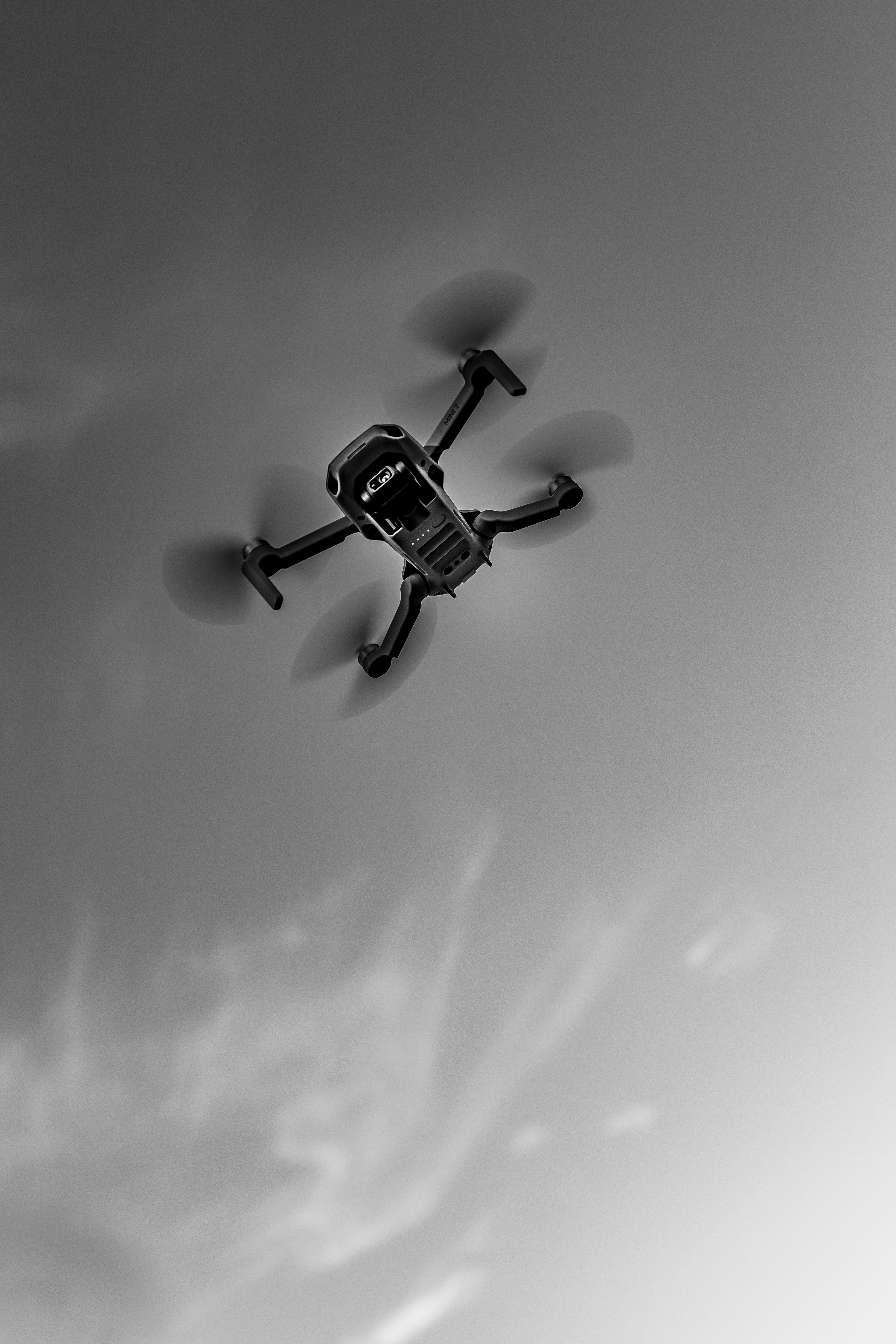 Drone hovering against a monochrome sky, showcasing its intricate design and propeller motion.
