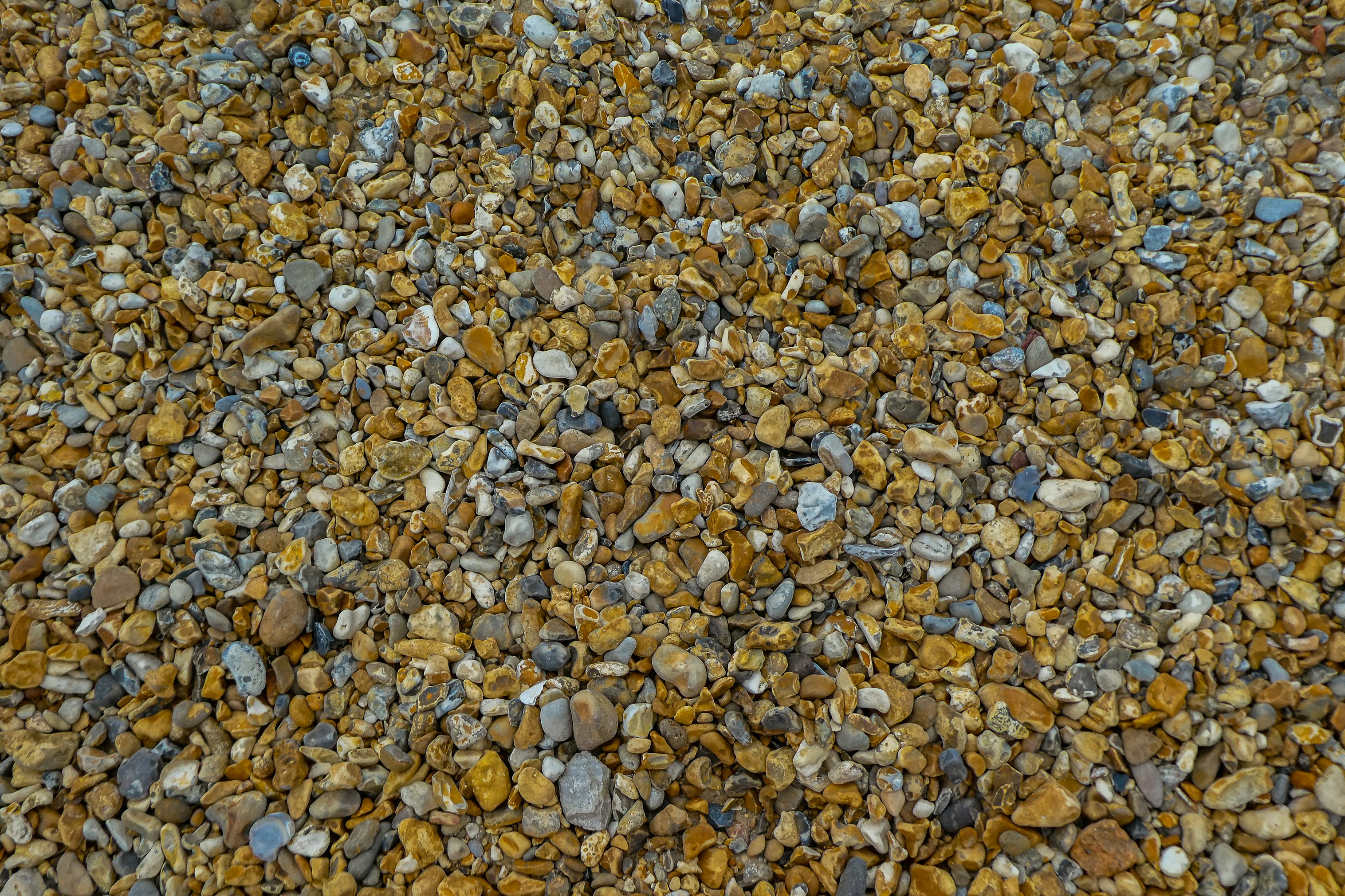 A close-up view of a textured surface composed of various small stones in shades of brown, gray, and yellow. This natural arrangement showcases the intricate details of gravel.