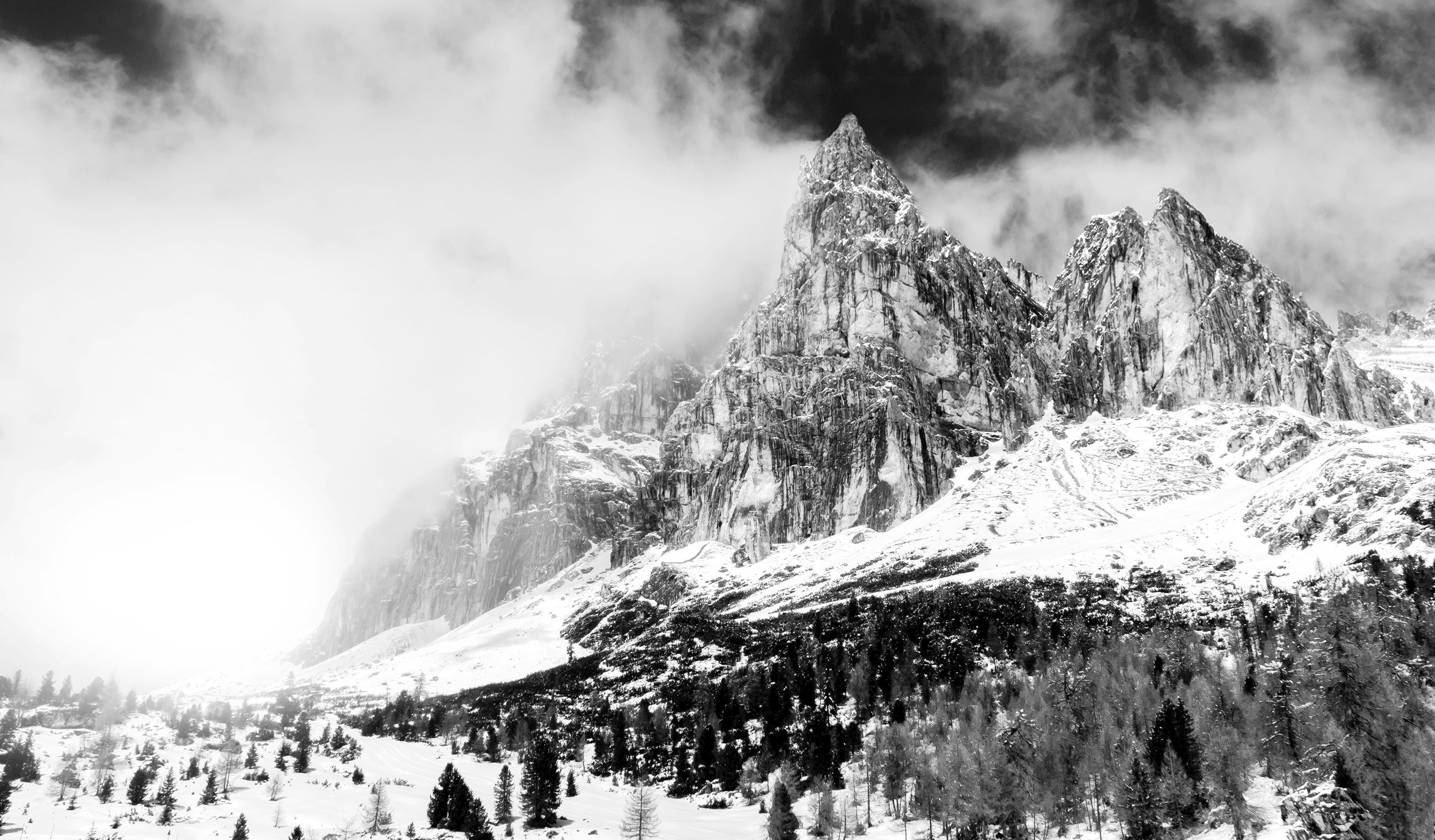 Majestic snow-capped mountains loom under a dramatic sky, enveloped in mist and mystery.