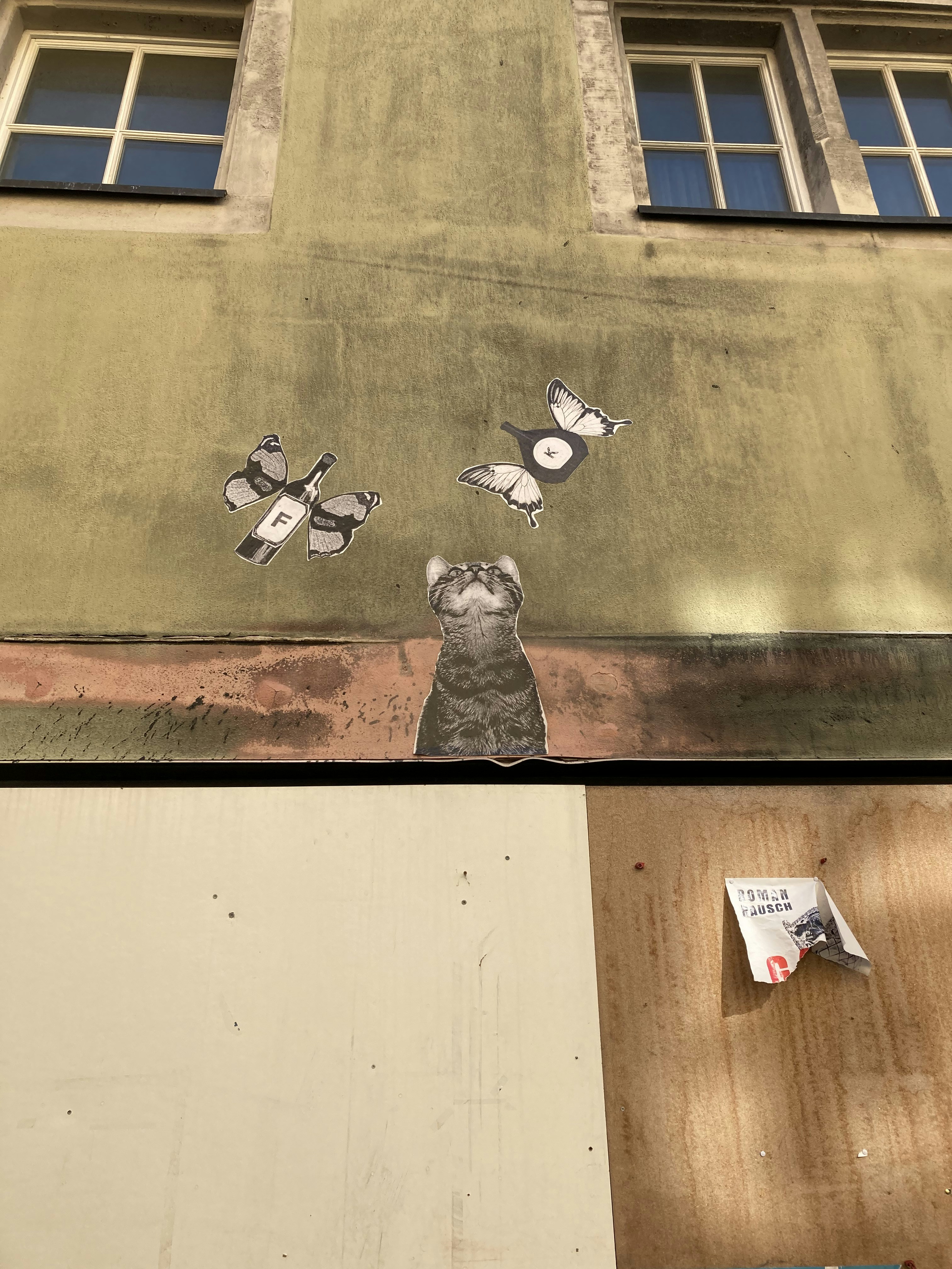 Street art featuring a dog surrounded by butterflies and a bottle, showcasing a playful interaction with the urban environment.