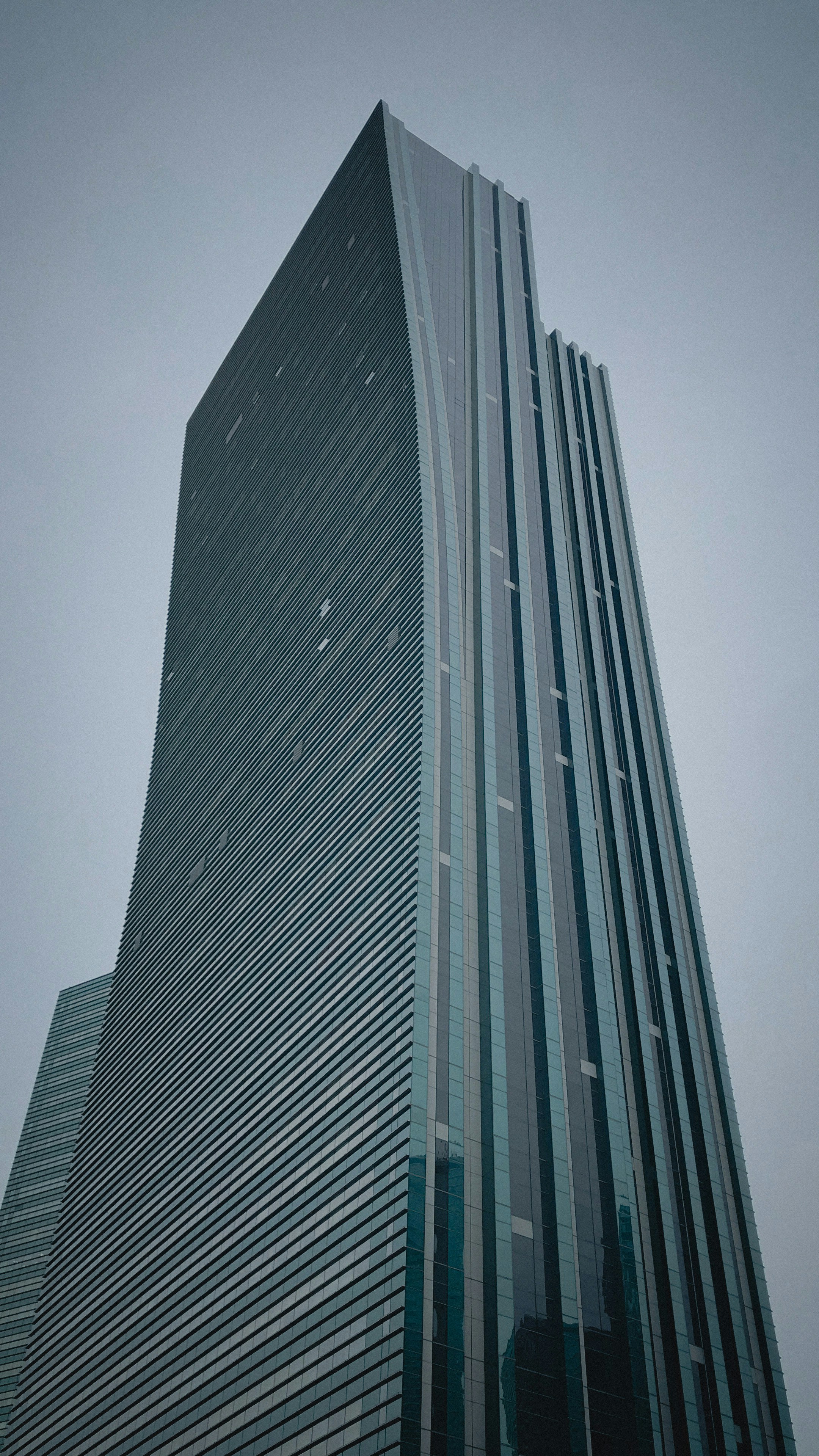 Sleek, modern skyscraper with a curved facade, reaching towards a cloudy sky. The architectural design emphasizes vertical lines and reflective glass surfaces.