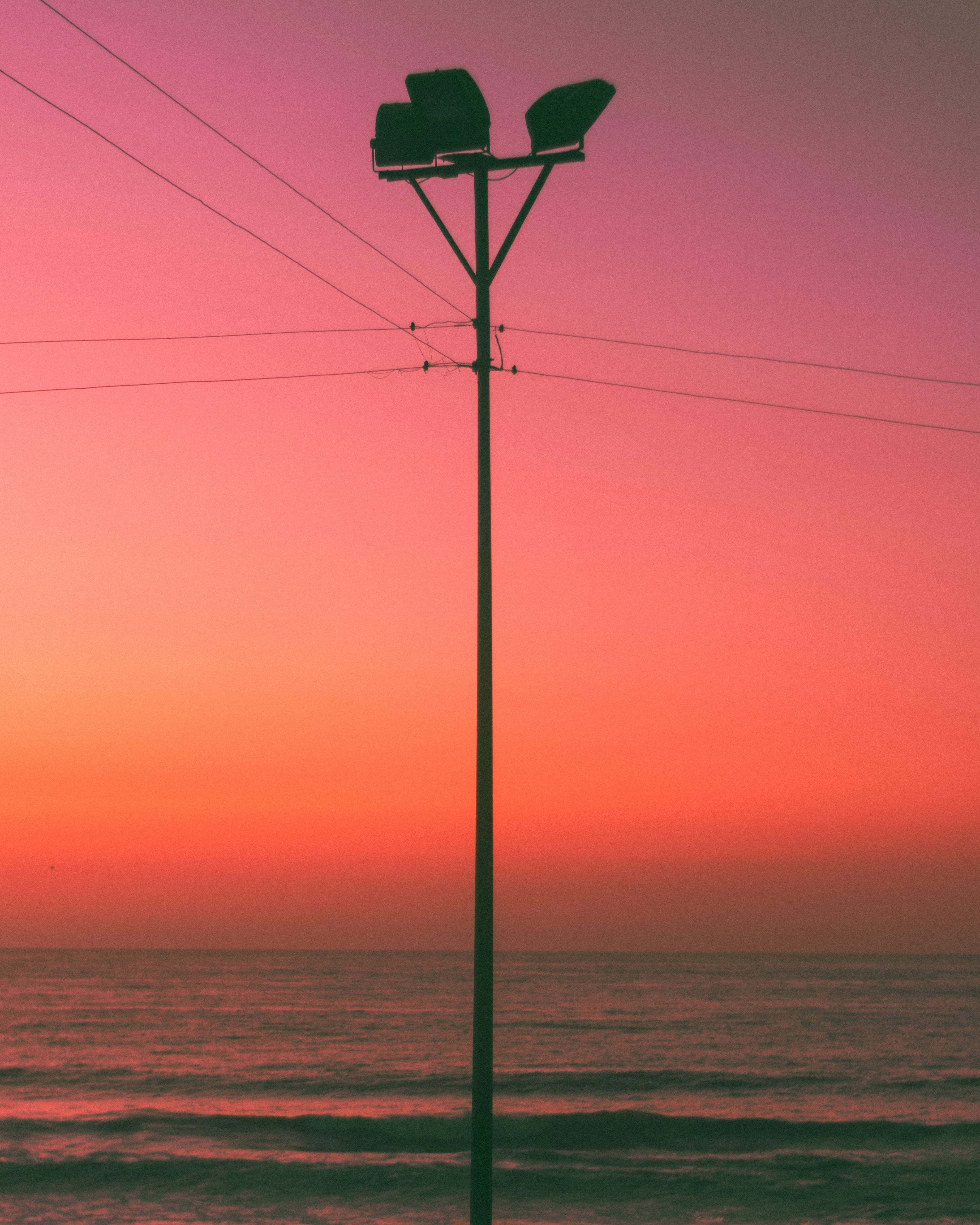 Streetlight silhouetted against a vibrant sunset over the ocean, with soft waves reflecting the warm hues of dusk.