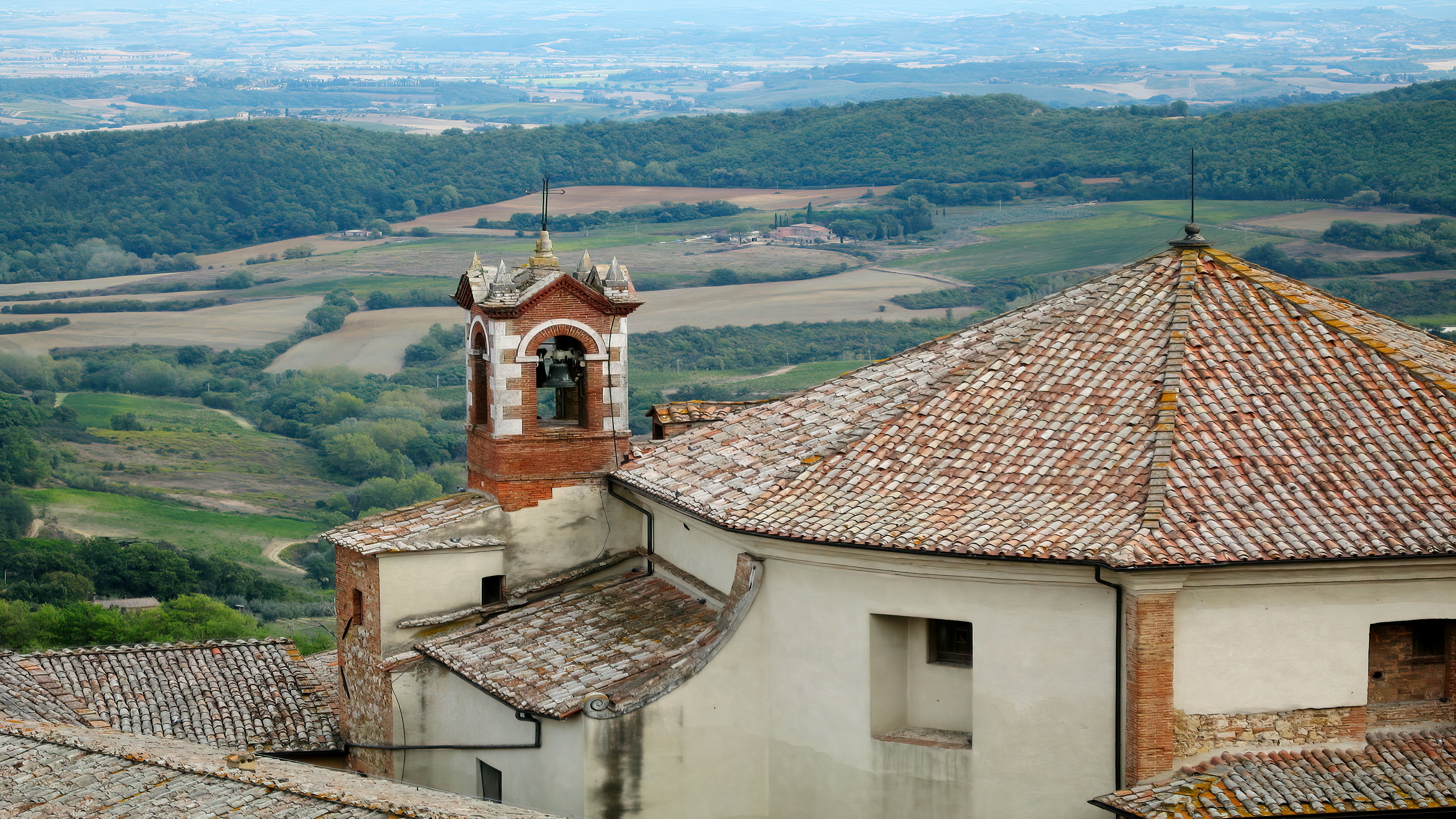 Historic bell tower rises above a picturesque landscape of rolling hills and vineyards, showcasing traditional architecture. A serene atmosphere envelops the scene.
