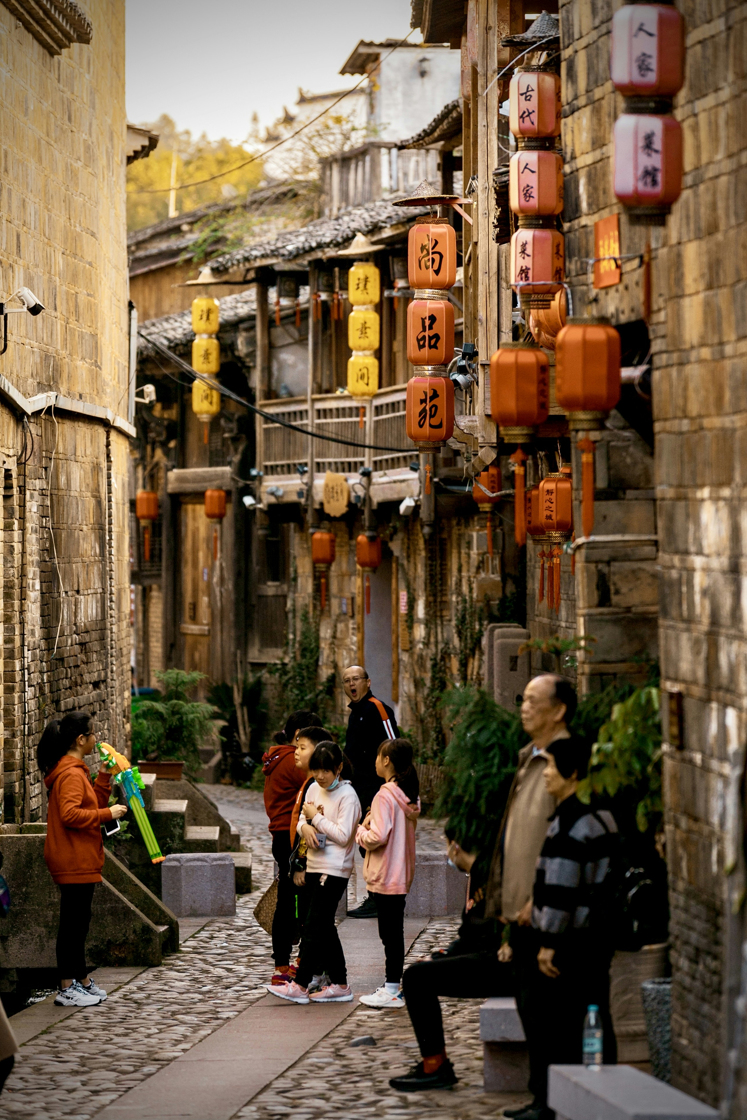 People walking through a narrow, lantern-adorned street in a historic town.