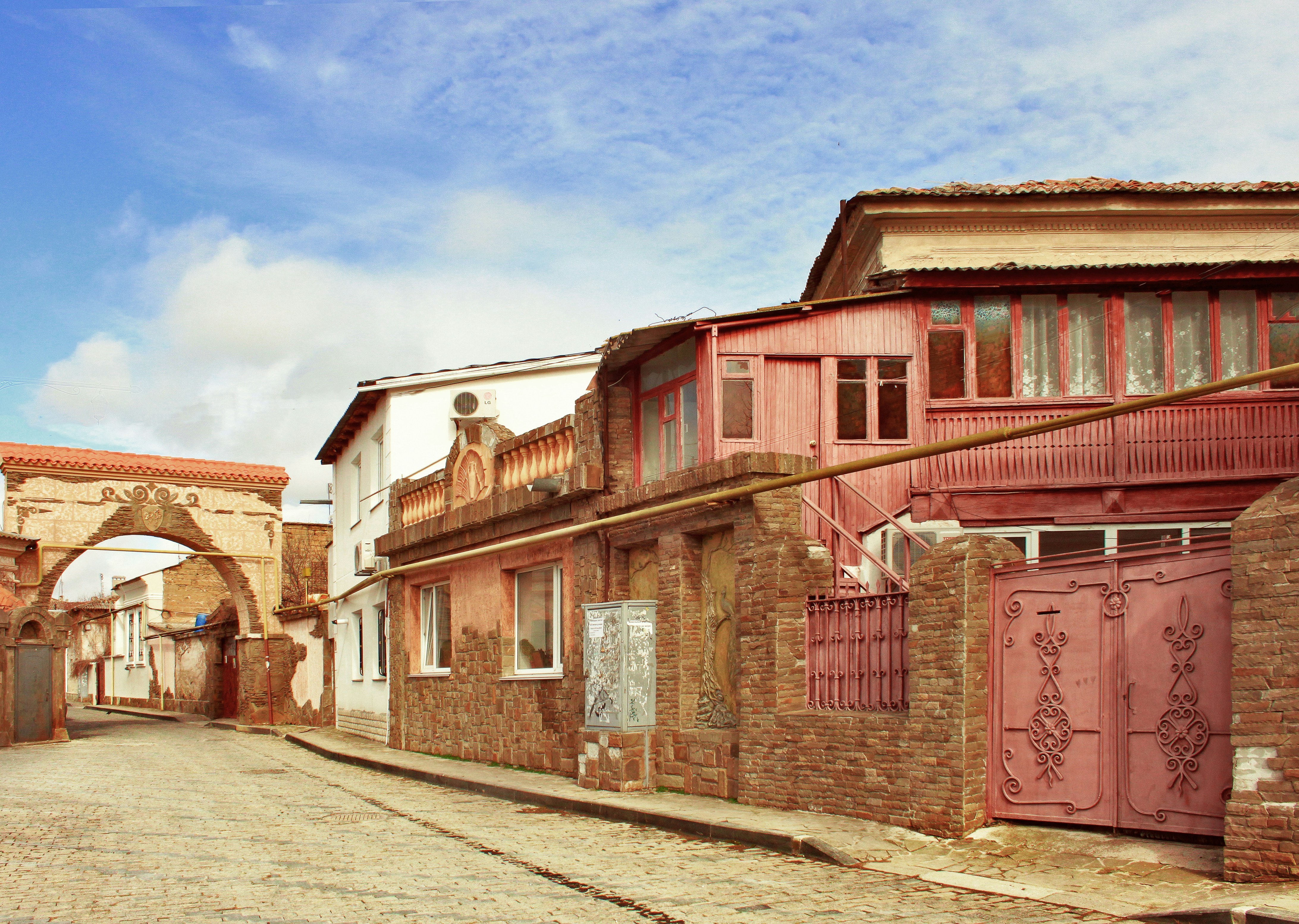Colorful historic buildings line a cobblestone street, framed by an ancient archway under a bright sky.