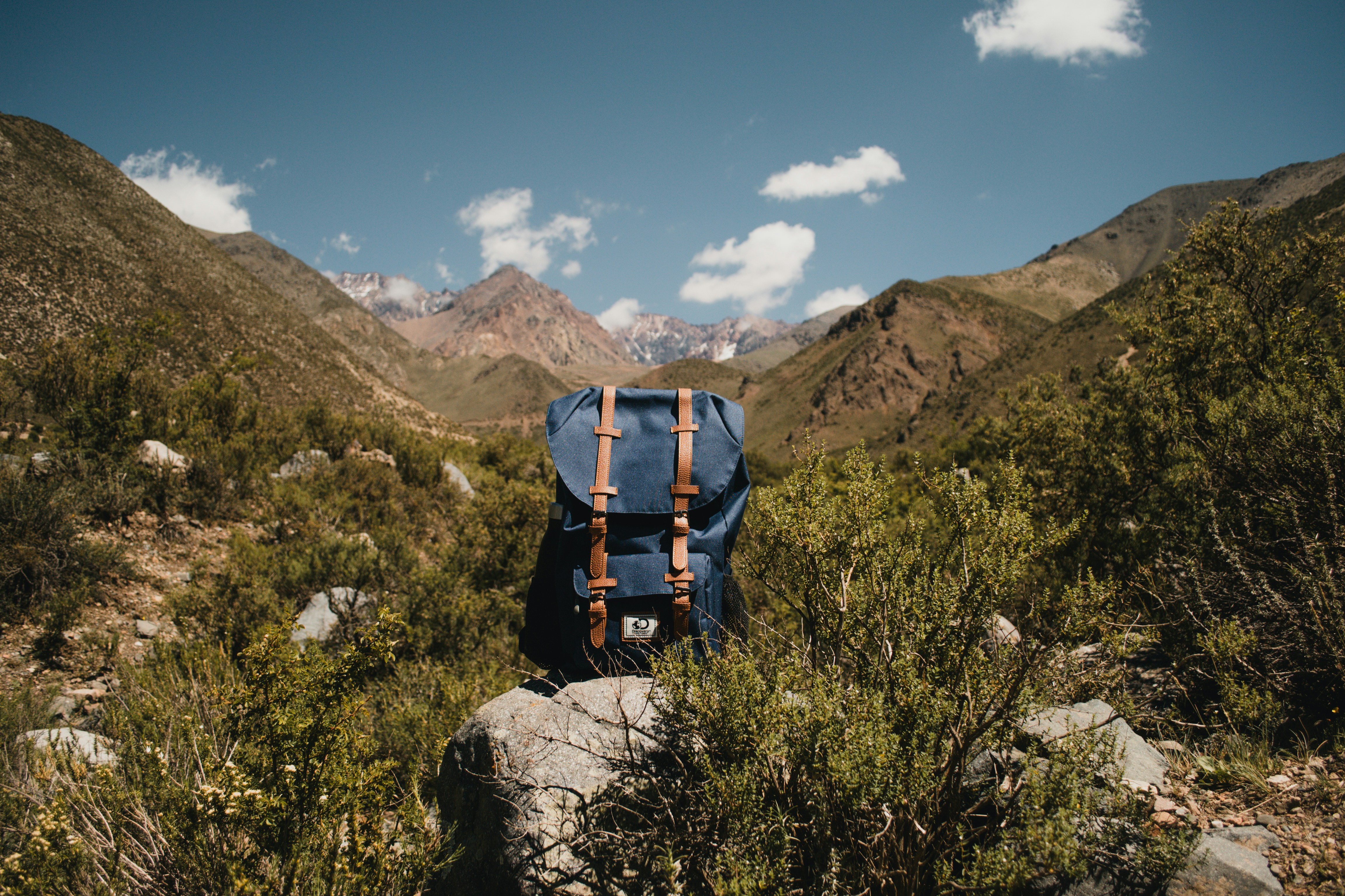 Blue backpack resting on a rock amidst arid mountain landscape under a clear sky.