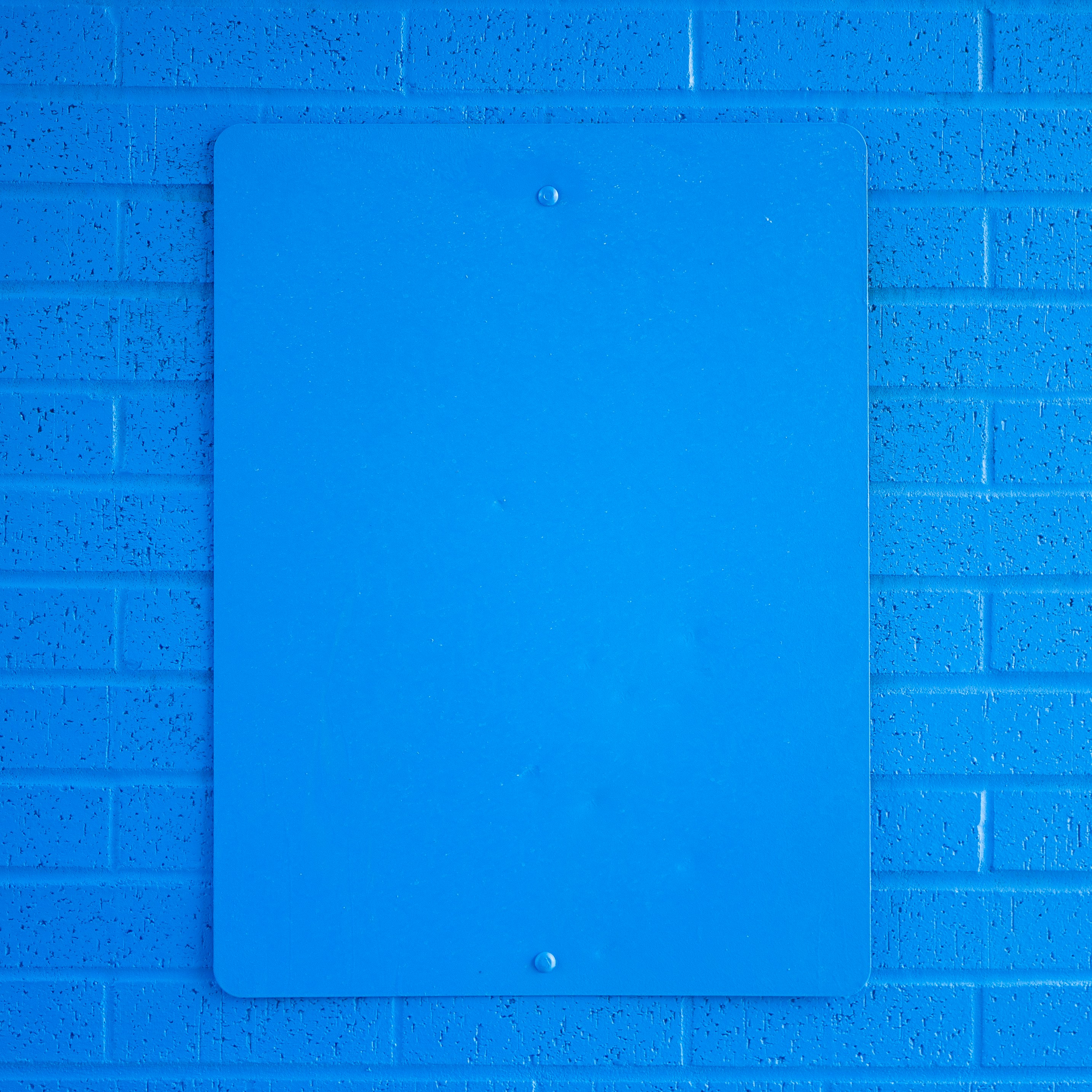 Solid blue wall with a blank sign mounted in the center, inviting creativity and expression.
