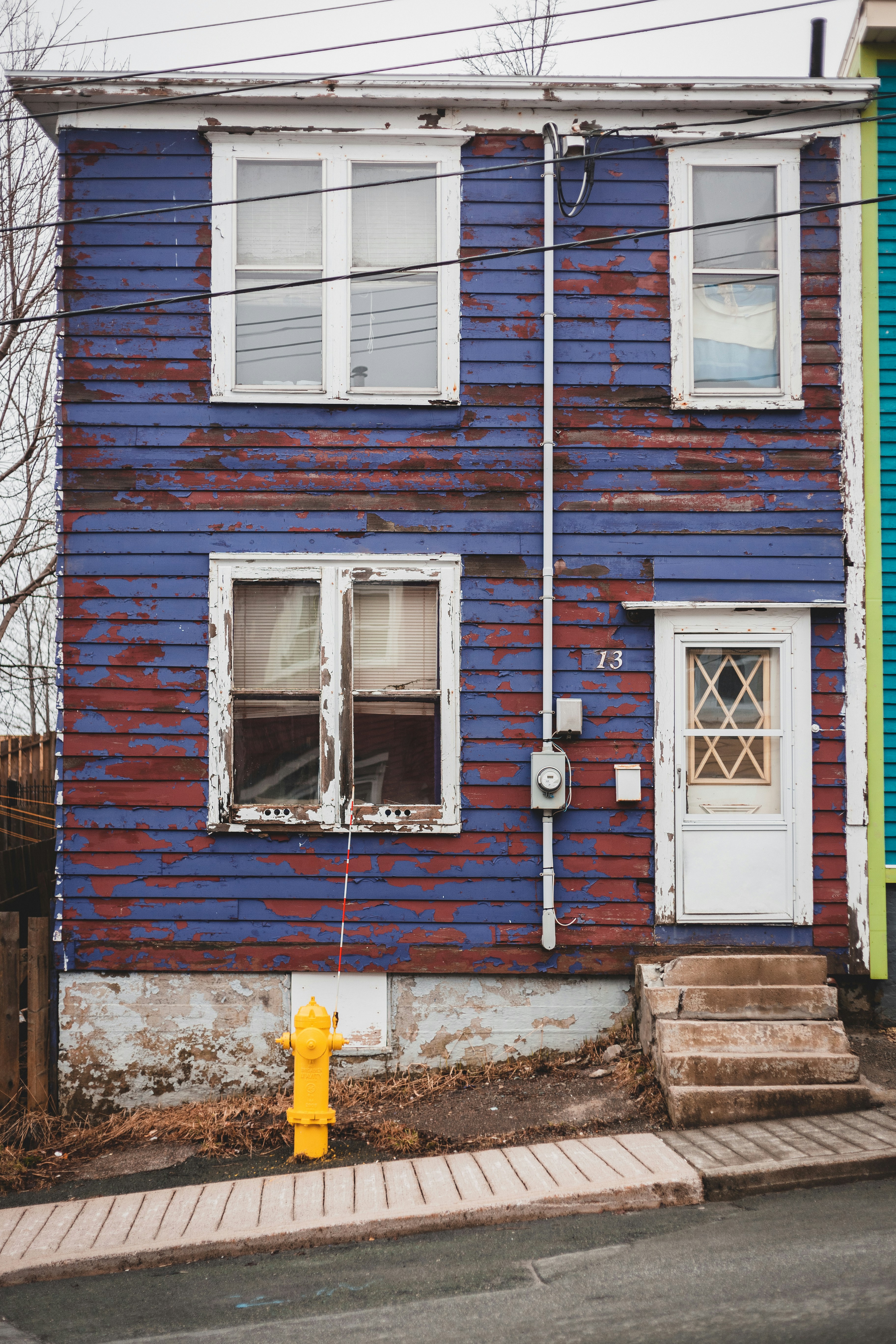 Weathered blue townhouse with peeling paint and yellow fire hydrant anchor