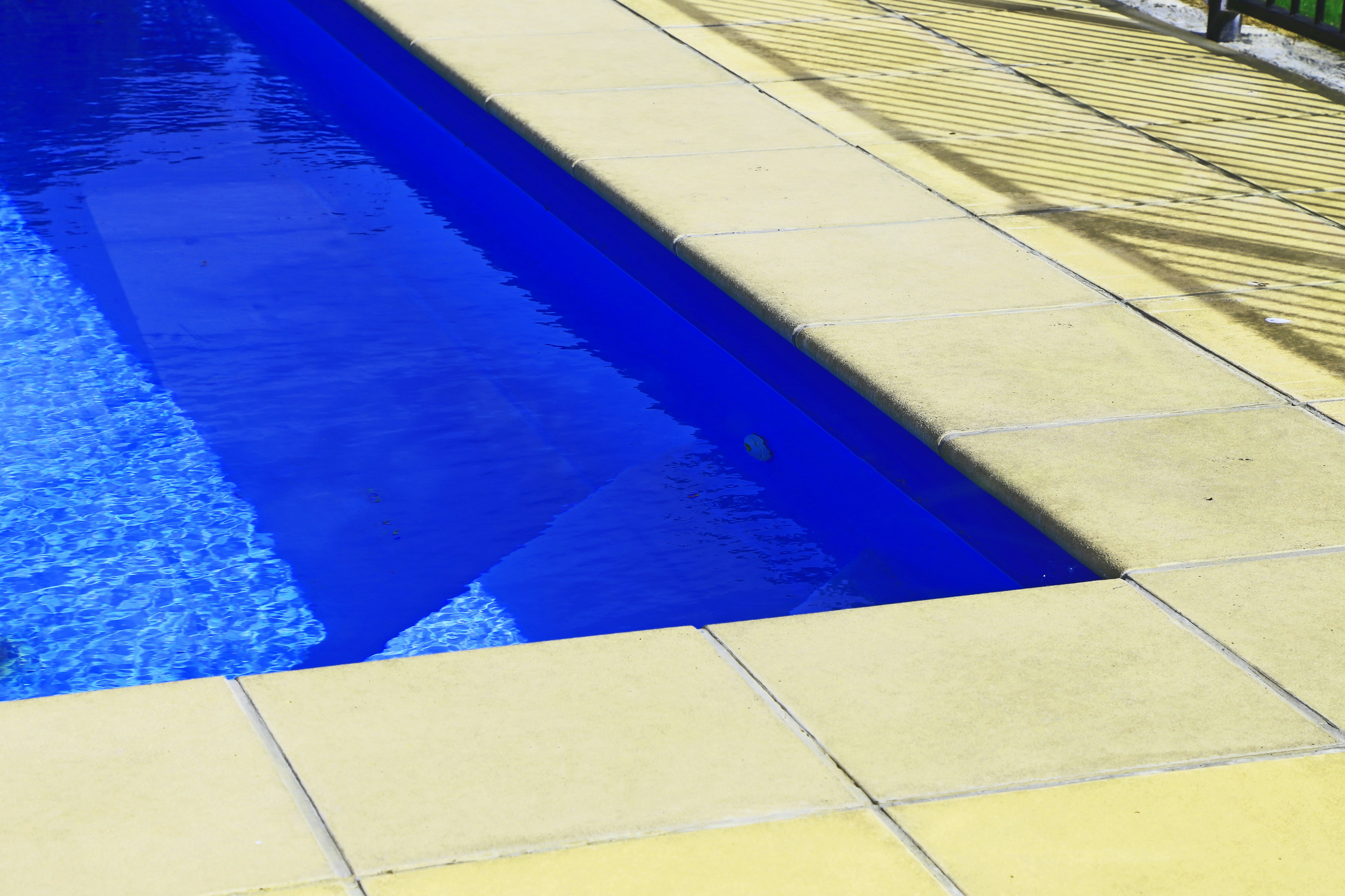 Vibrant blue swimming pool bordered by bright yellow tiles, reflecting sunlight and creating a tranquil atmosphere.