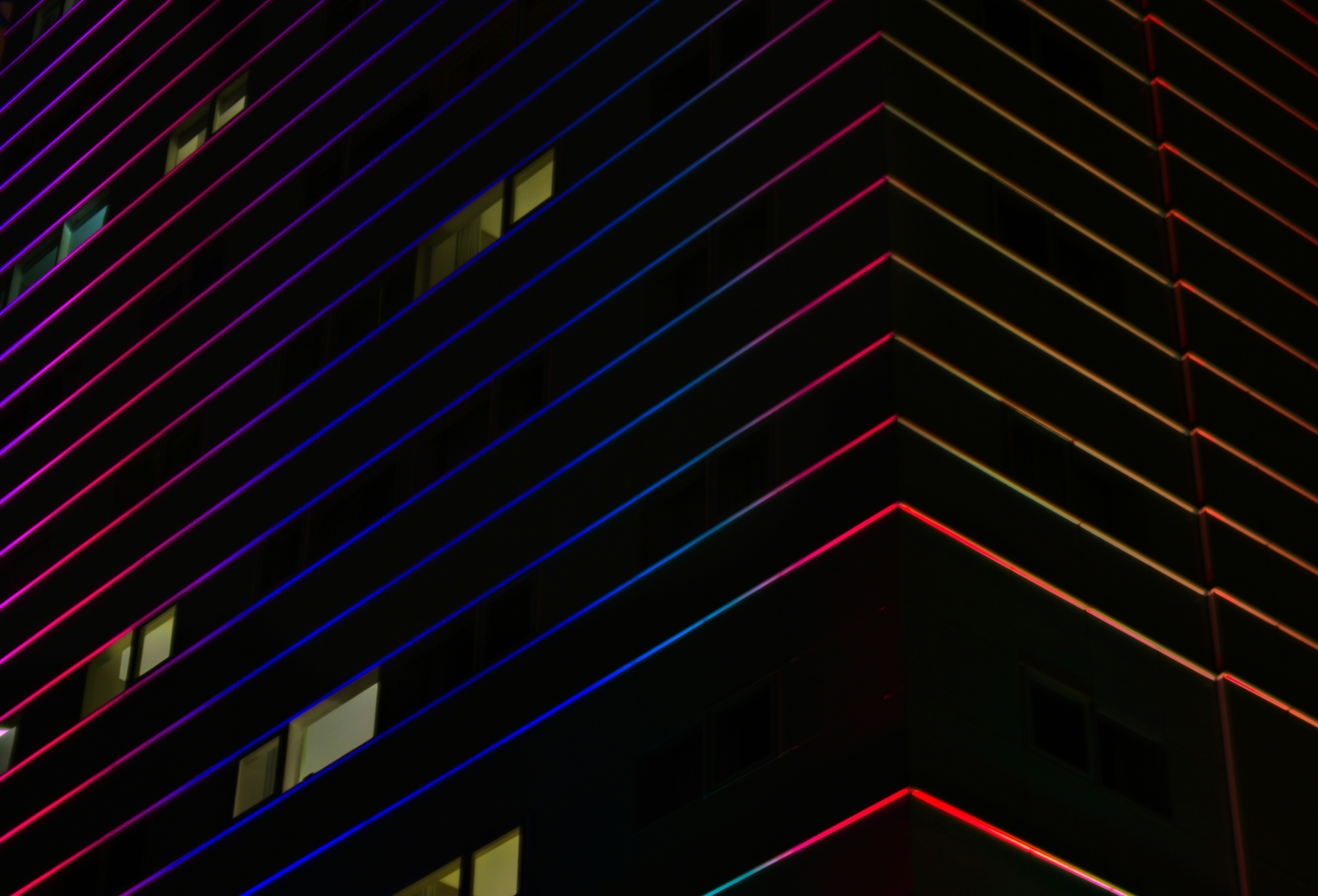 Vibrant neon lines illuminate the facade of a contemporary building, creating a striking visual contrast against the dark night sky.