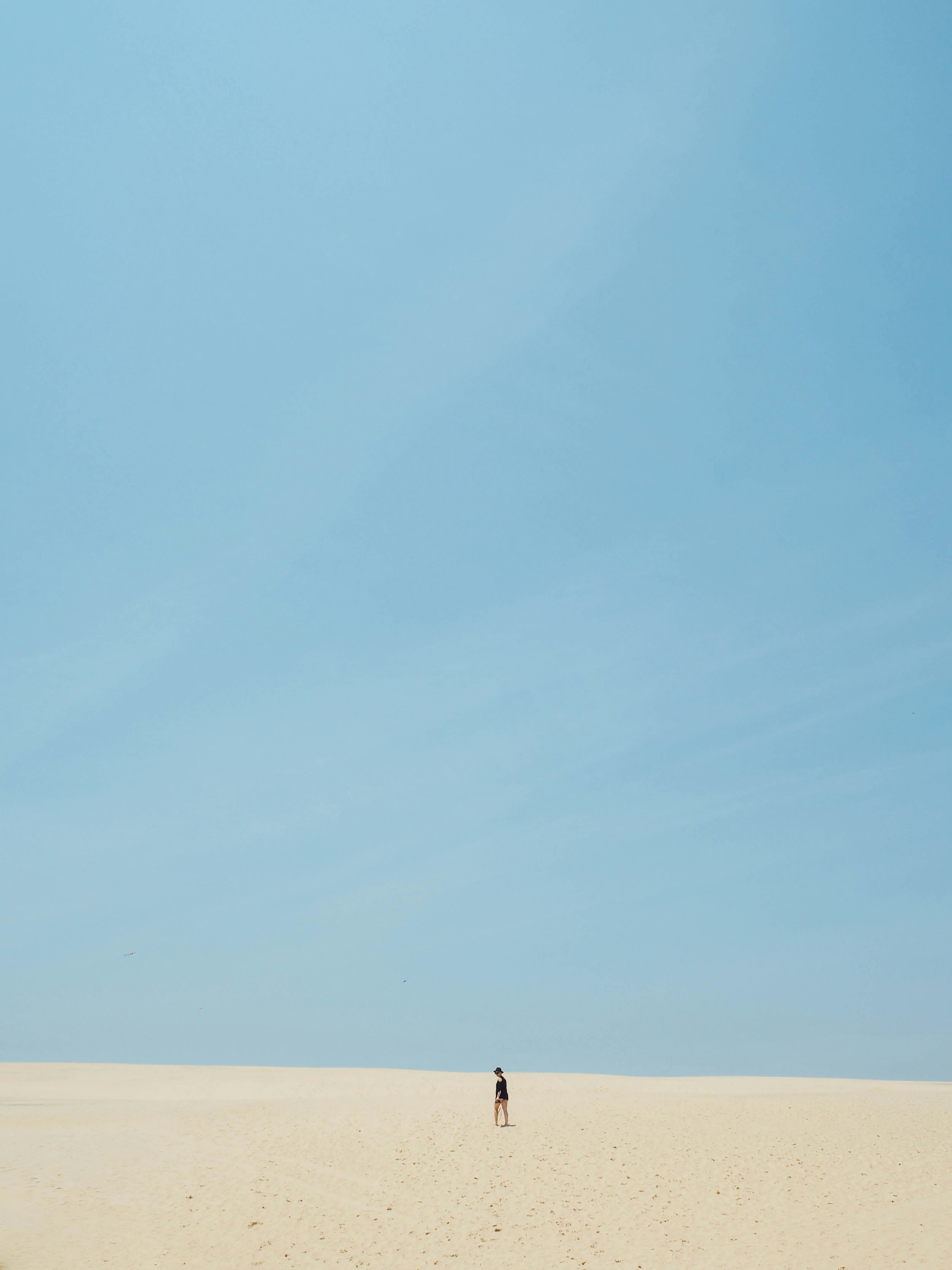 A lone figure stands on a vast expanse of sand under a clear blue sky, emphasizing the sense of solitude and adventure.