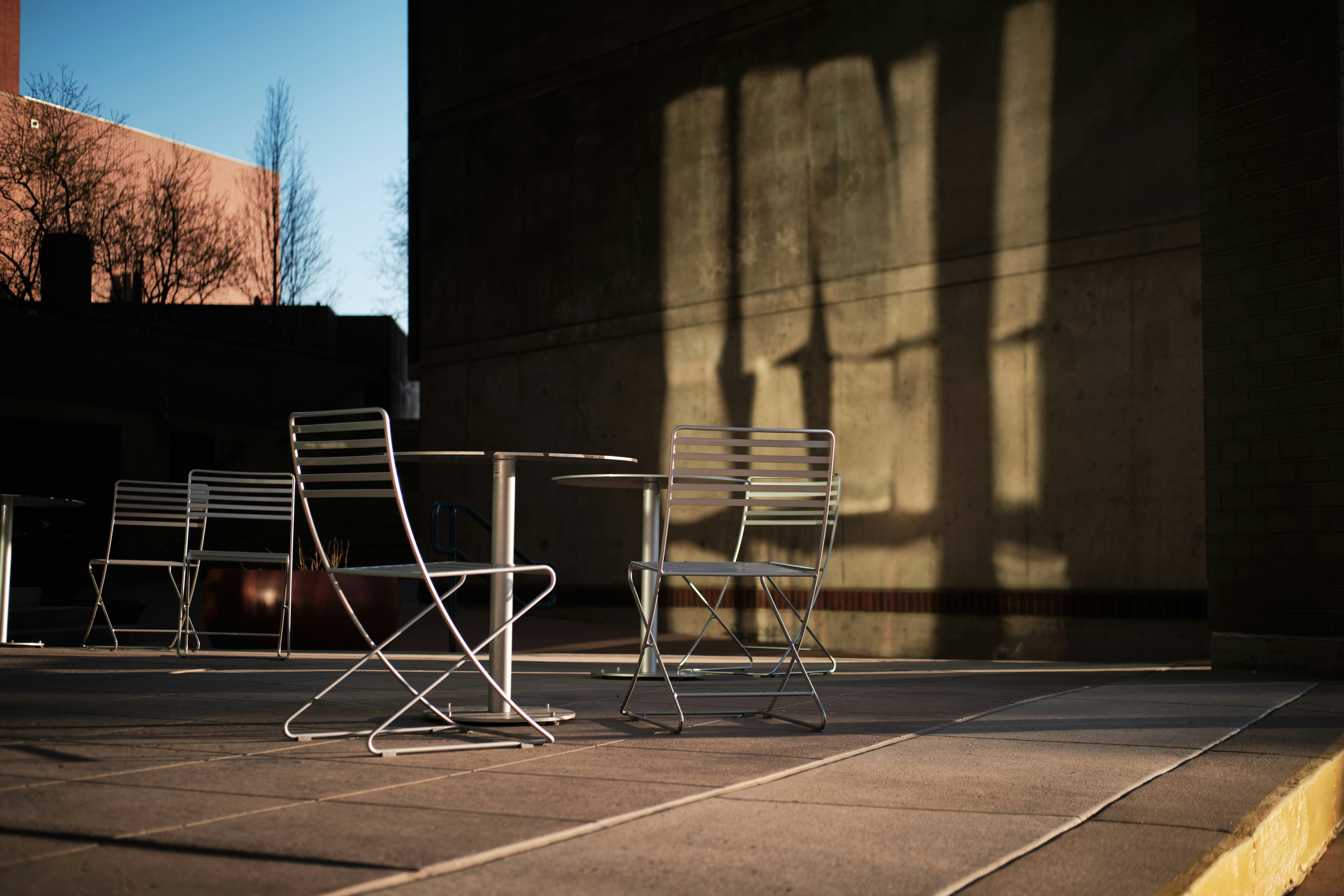 Minimalist outdoor seating arrangement casting long shadows on a sunlit pavement.