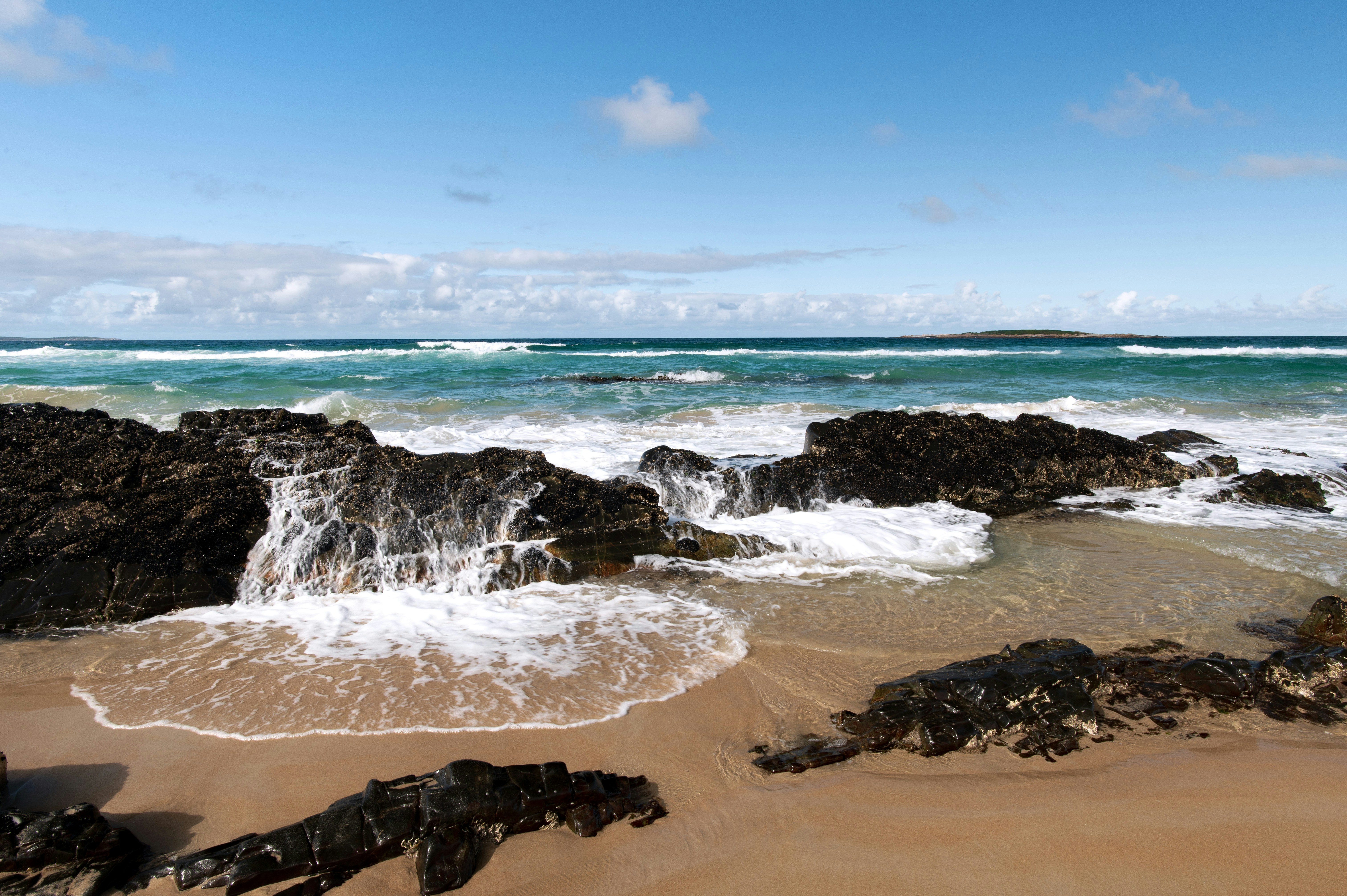 A wave forms a pool of water after washing over a rock. Beaumaris Beach, Tasmania, Australia. | ocean waves crashing on shore during daytime