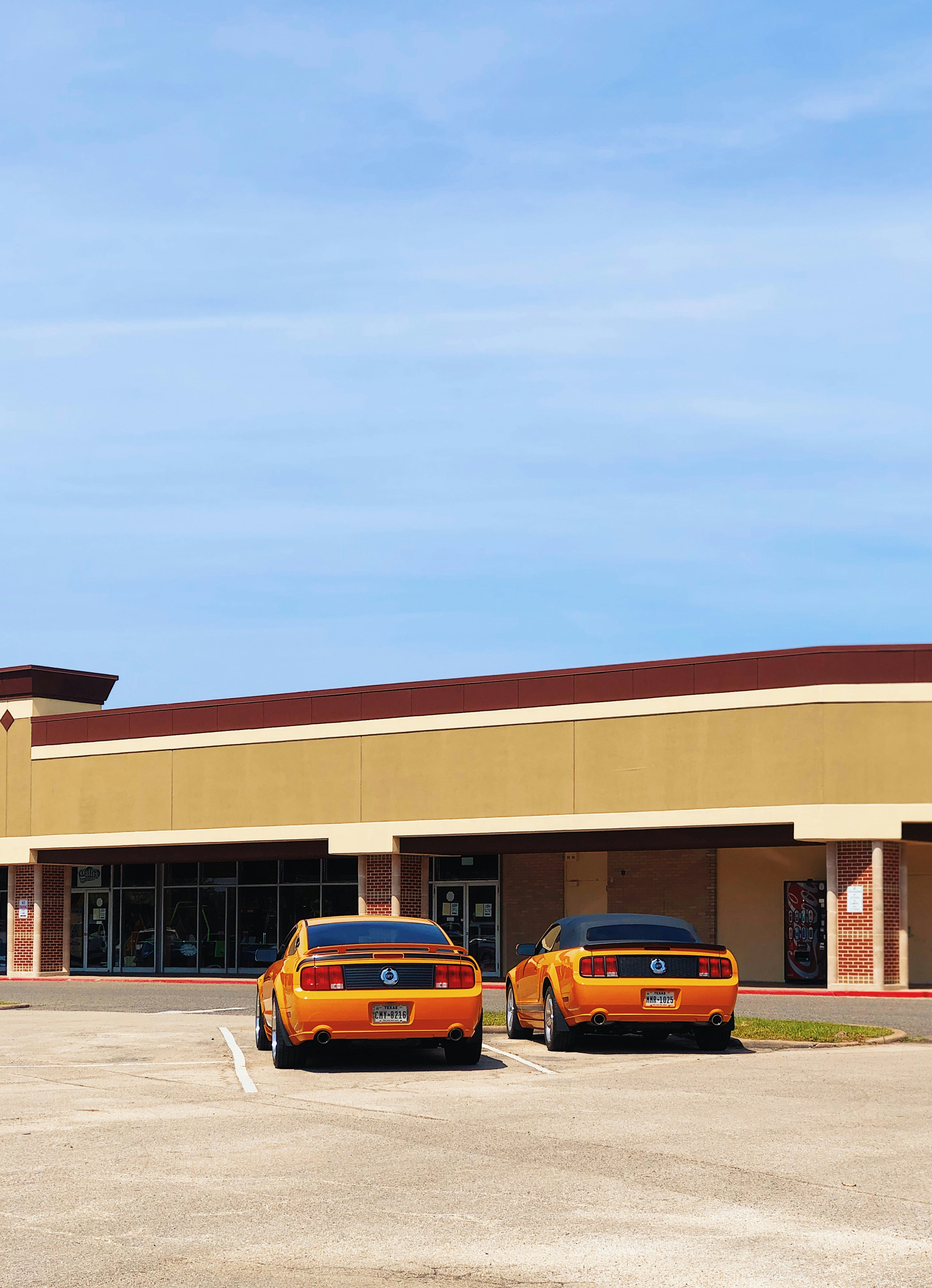 Twin Orange Coupes Resting Before a Beige Strip Mall