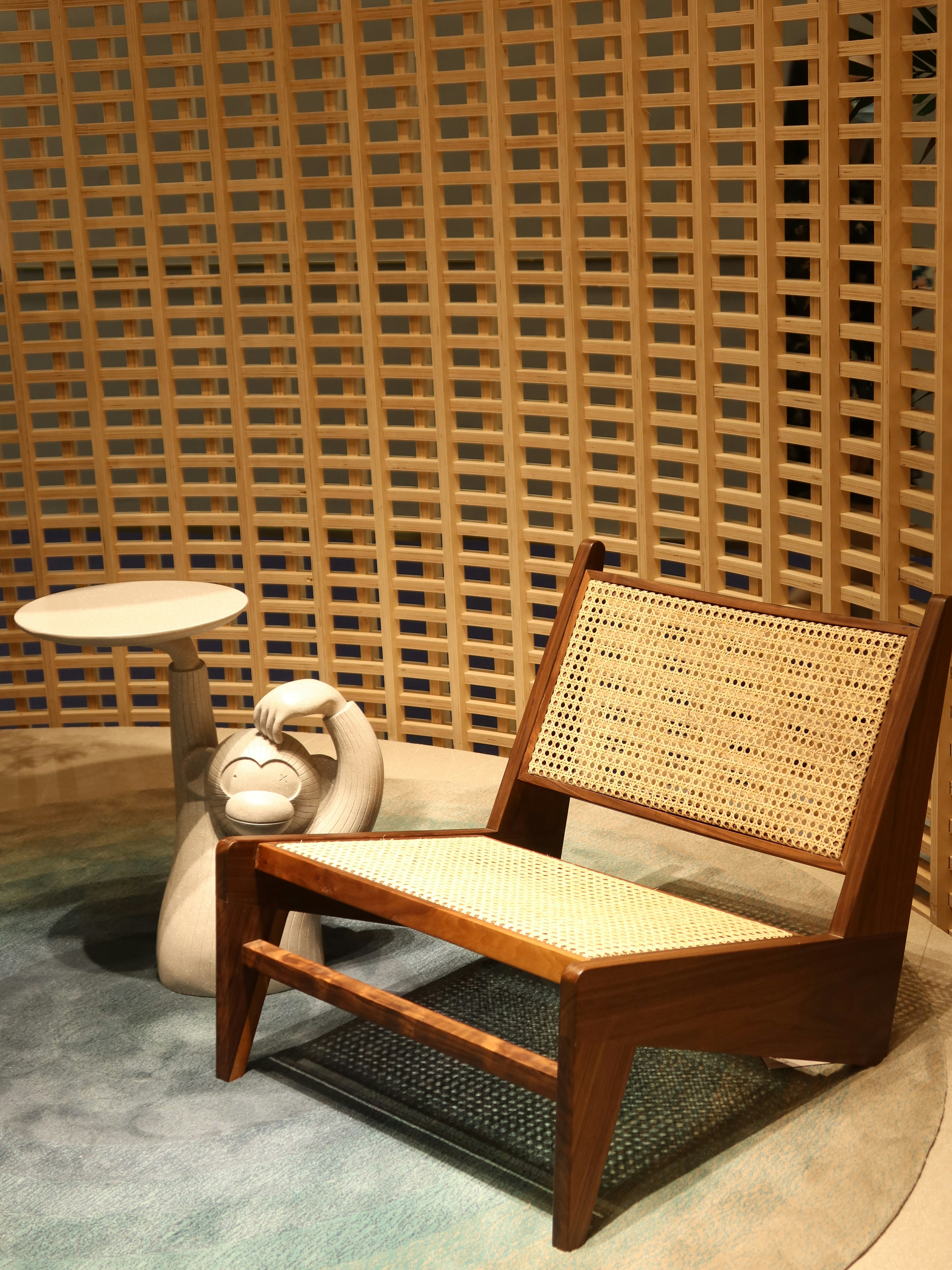 Stylish wooden chair paired with a playful sculpture and a round side table, set against a woven backdrop. A modern design that invites relaxation.