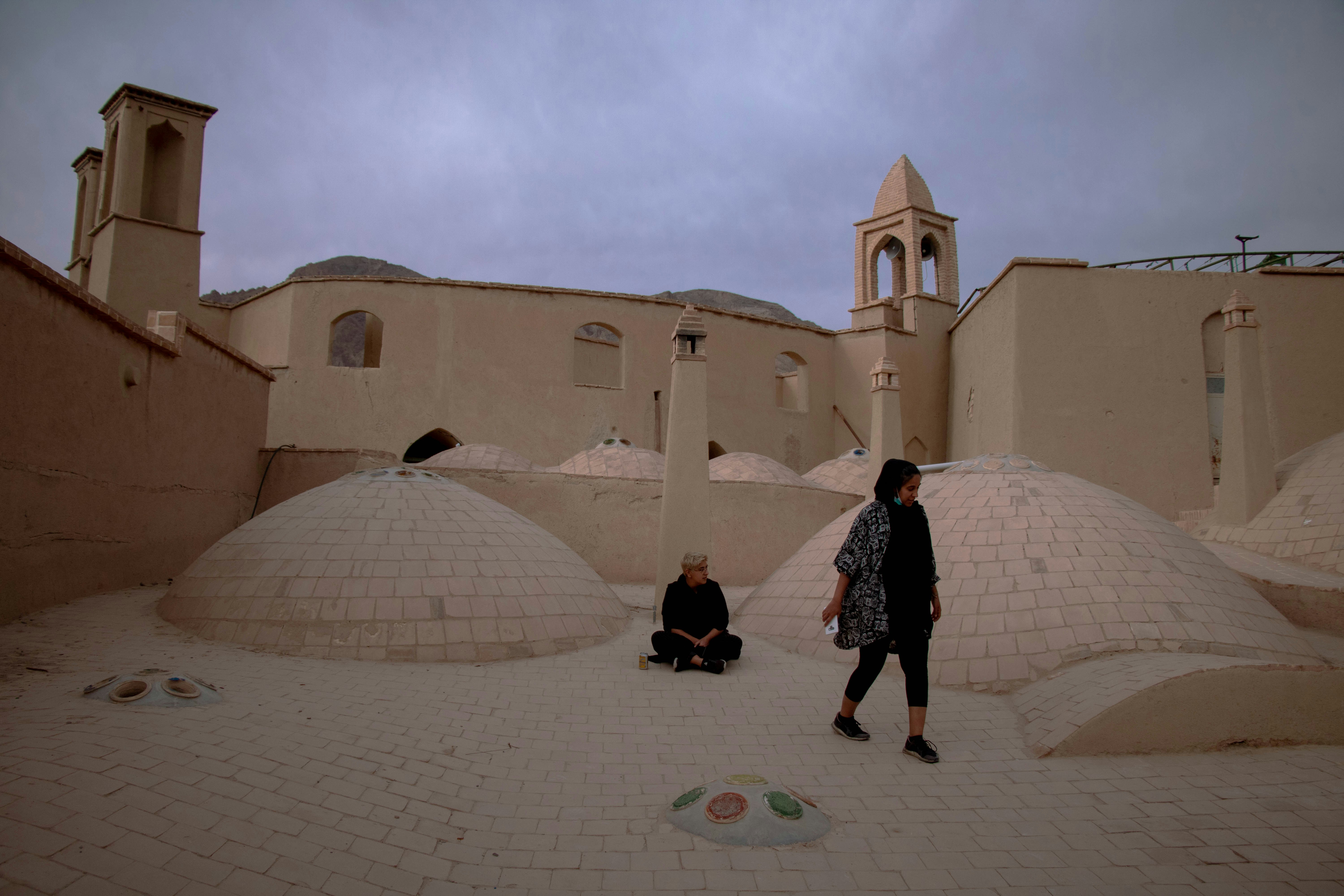 Two figures traverse a historic landscape marked by domed structures and ancient walls, embodying the spirit of exploration.