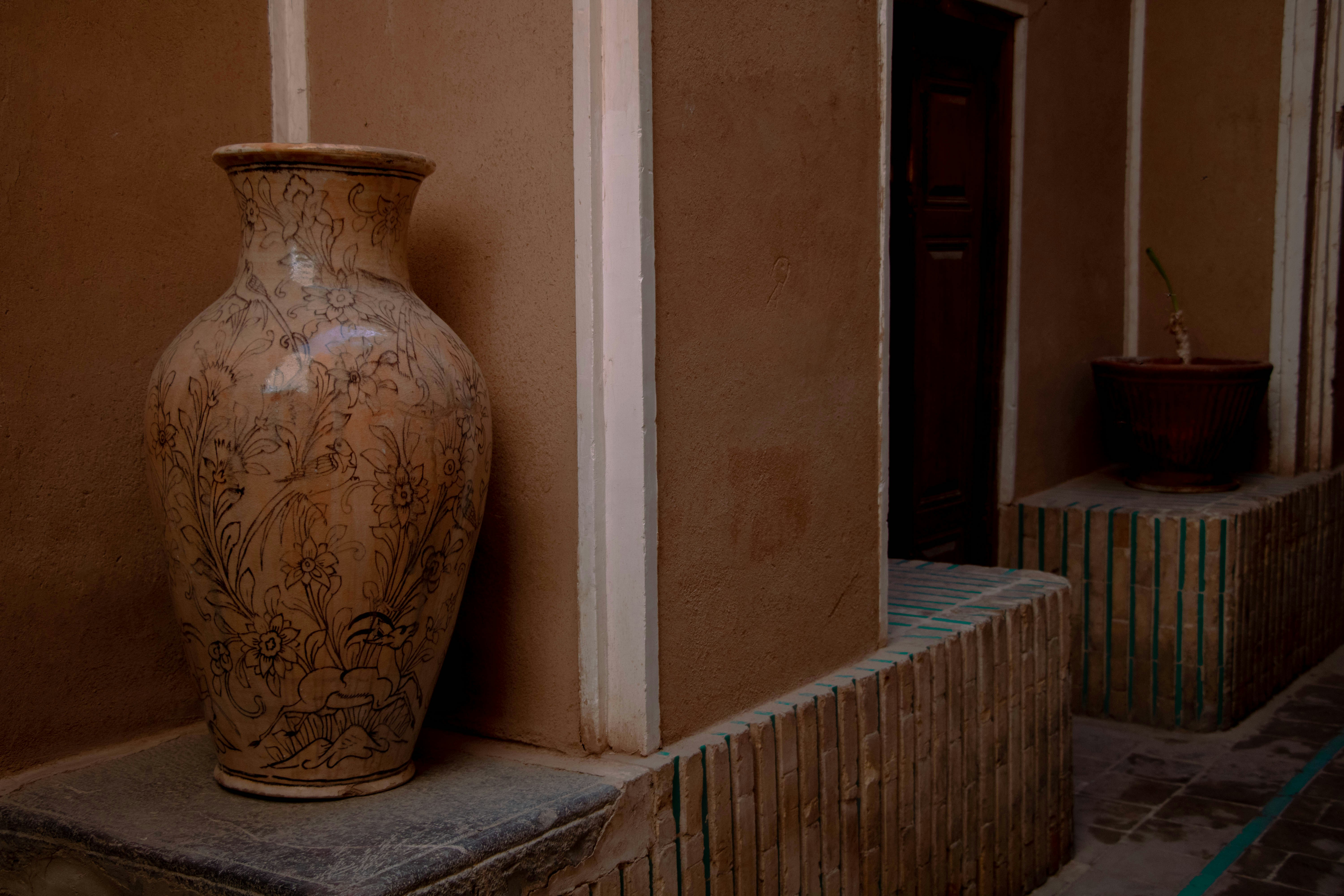 Intricately designed clay pot resting against a textured wall in a sunlit corridor, embodying cultural craftsmanship.