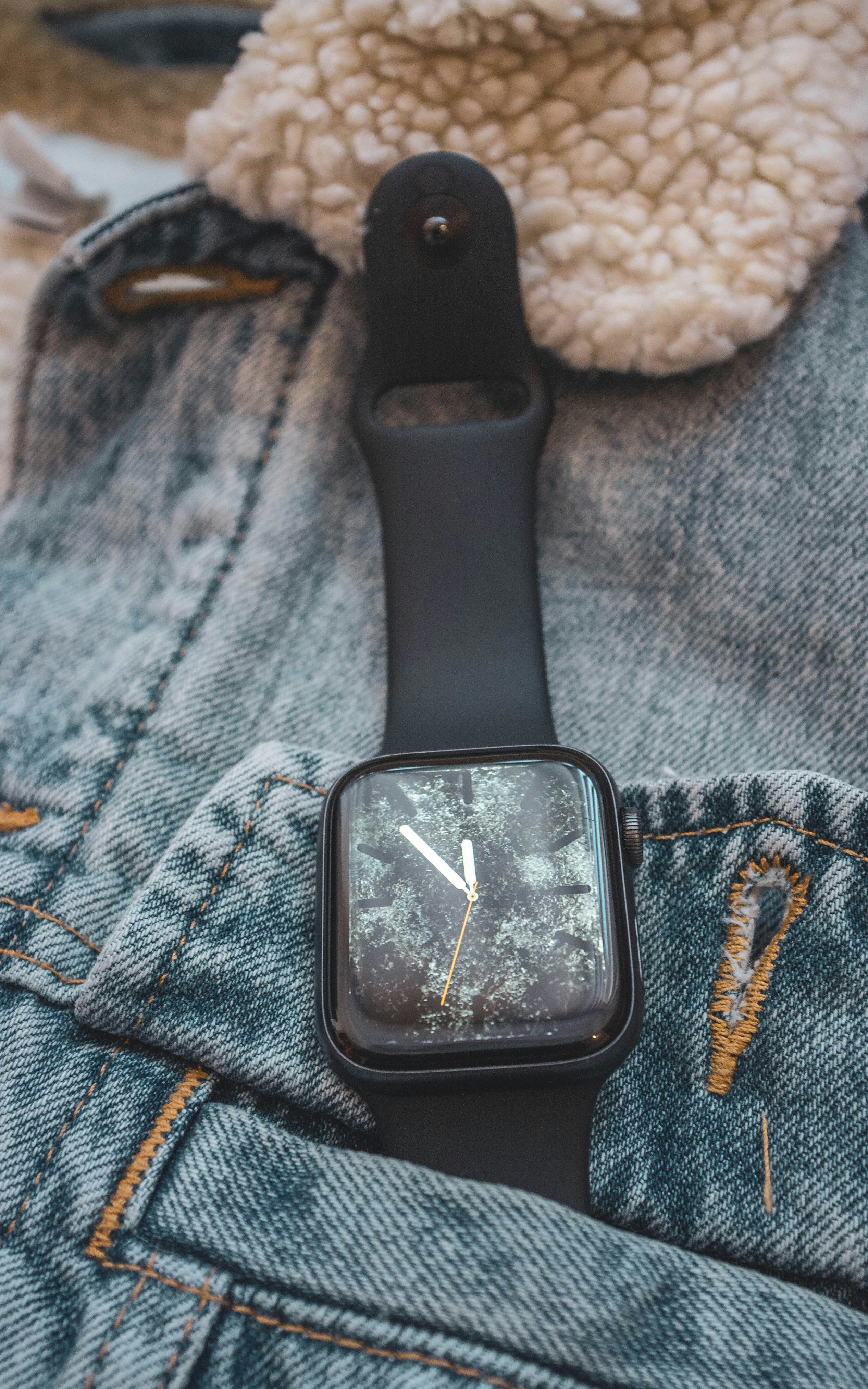 A sleek smartwatch resting on a denim jacket, showcasing a textured dial that contrasts with the fabric's ruggedness.