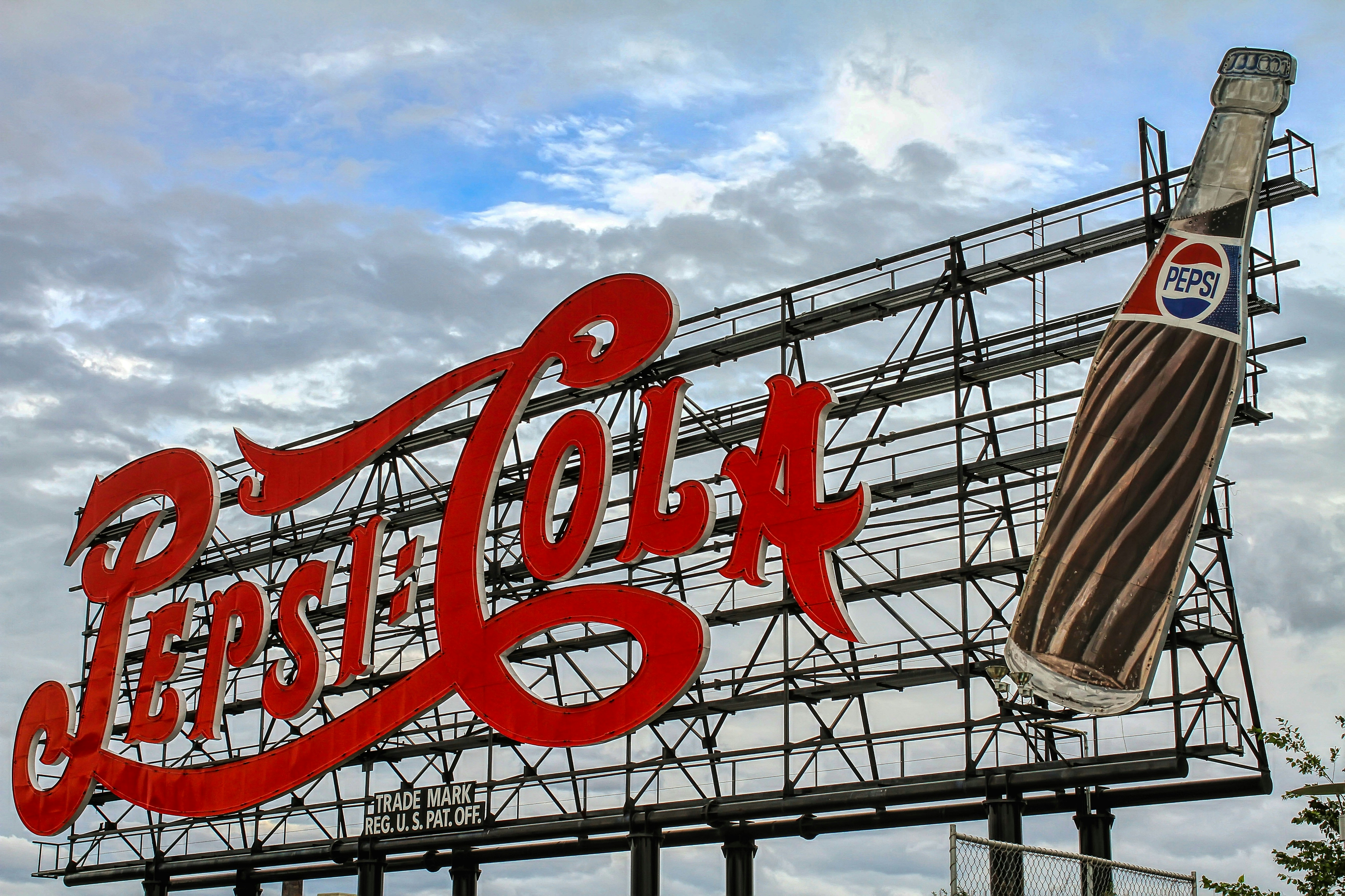 Vintage Pepsi-Cola billboard showcasing the iconic logo and a classic bottle against a dramatic sky.