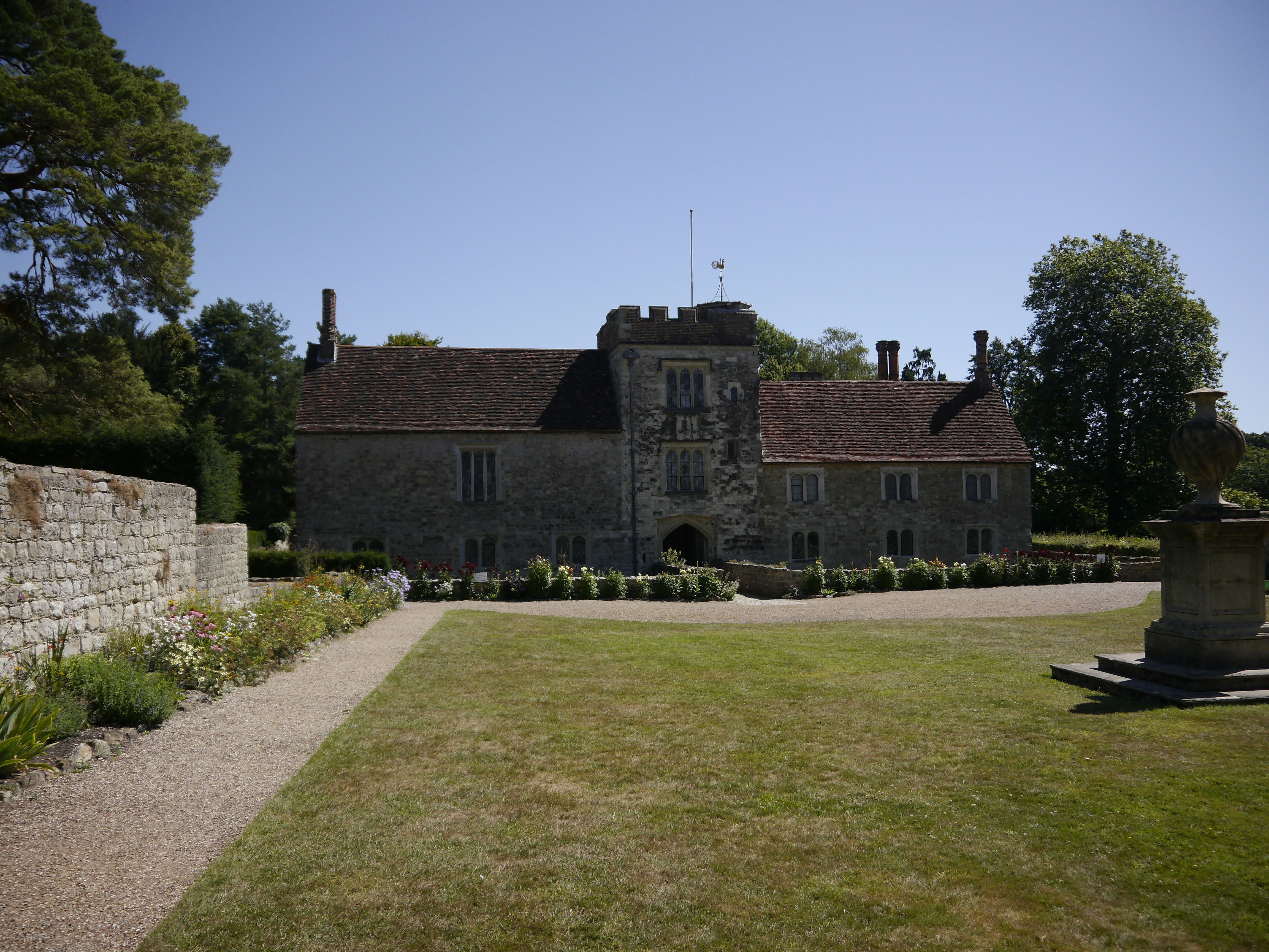 Historic stone manor surrounded by vibrant gardens and lush greenery under a clear blue sky.
