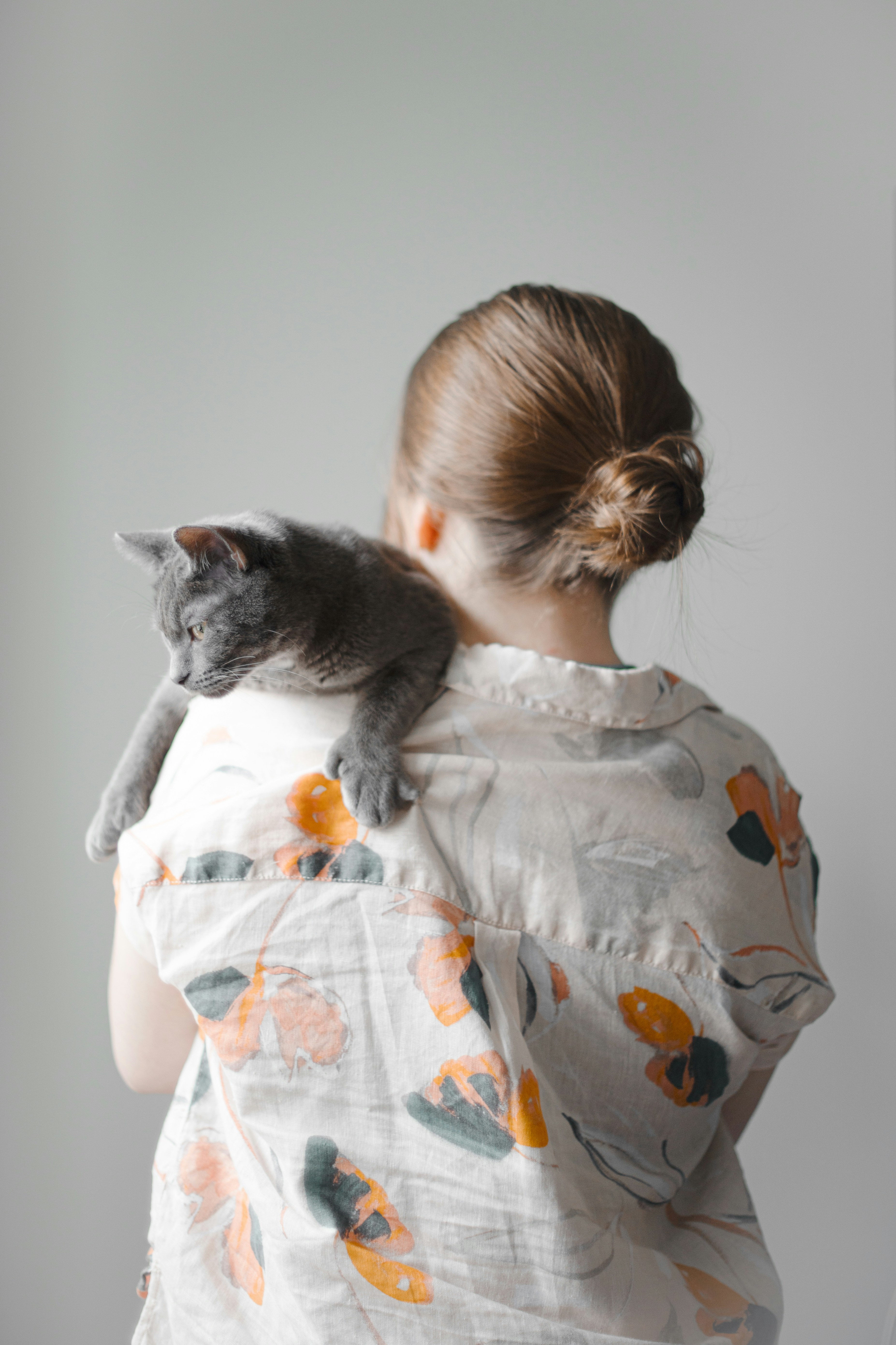 Person with a floral shirt carries a grey cat on their shoulder, showcasing a warm and intimate moment. Soft lighting enhances the serene atmosphere.