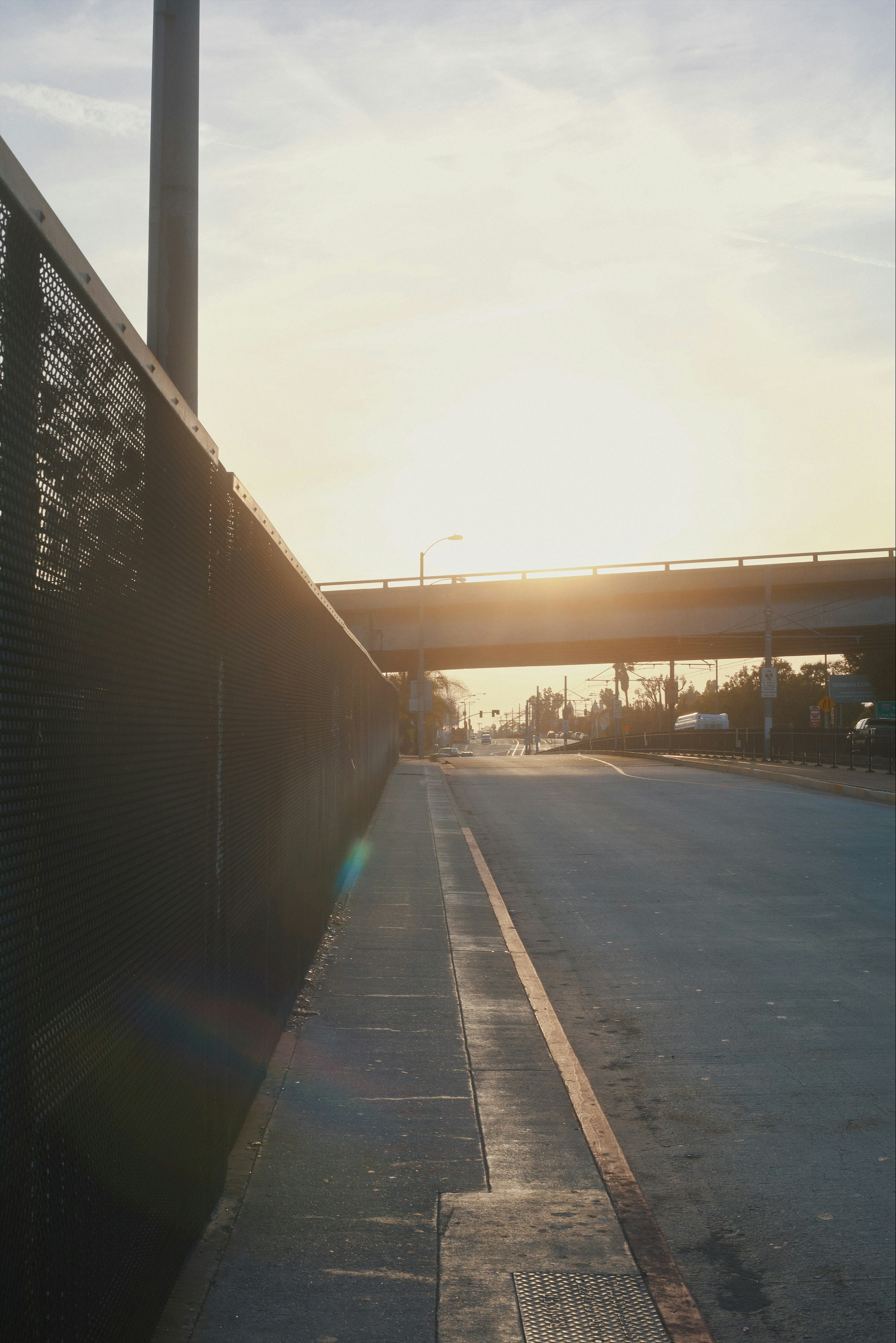 Golden Hour Trace: A Quiet City Street Framed by Fence and Overpass