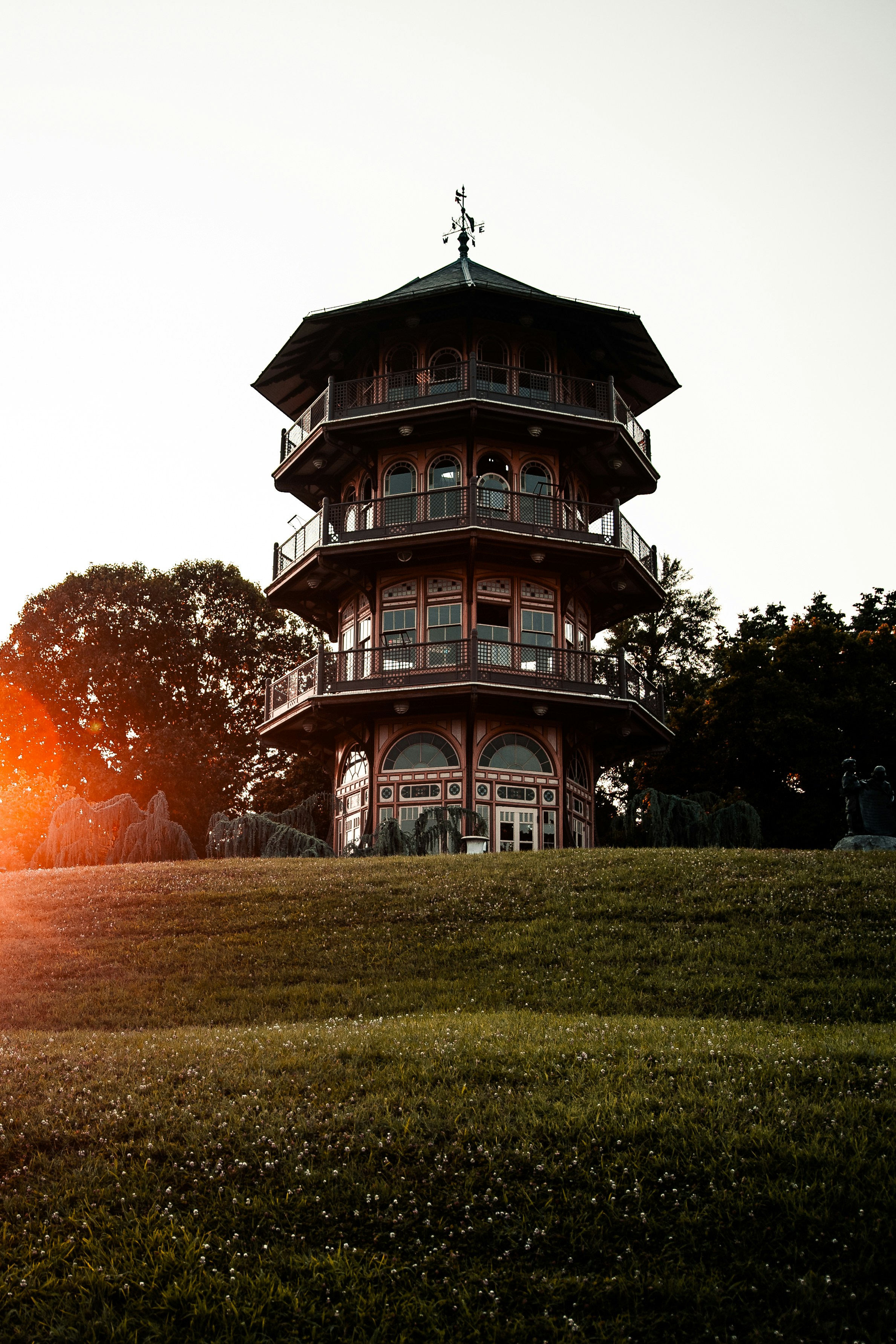 A traditional pagoda stands majestically on a grassy hill, illuminated by the warm glow of the setting sun, surrounded by lush trees.