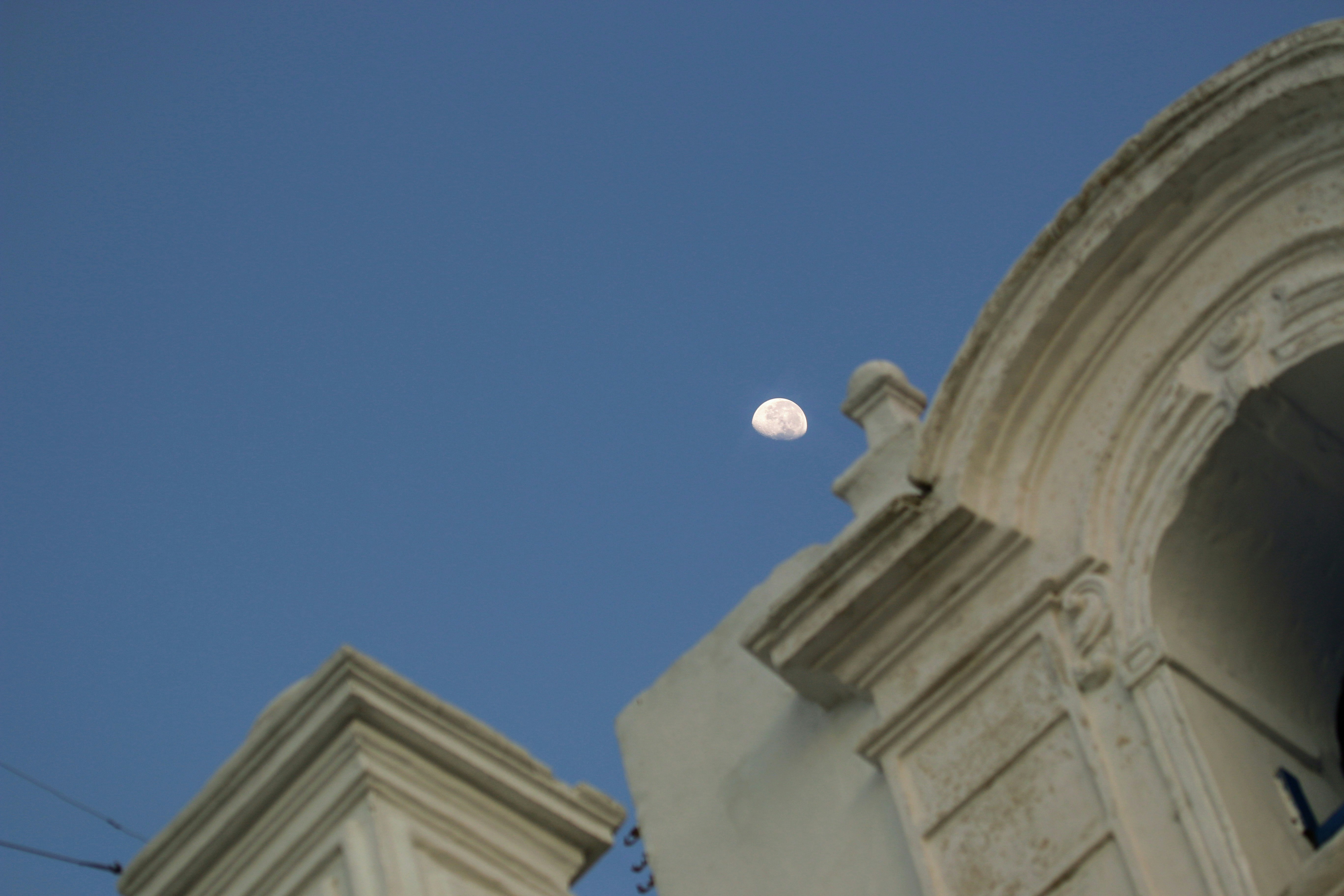 Ornate architectural details of a building with the moon visible in the clear blue sky.
