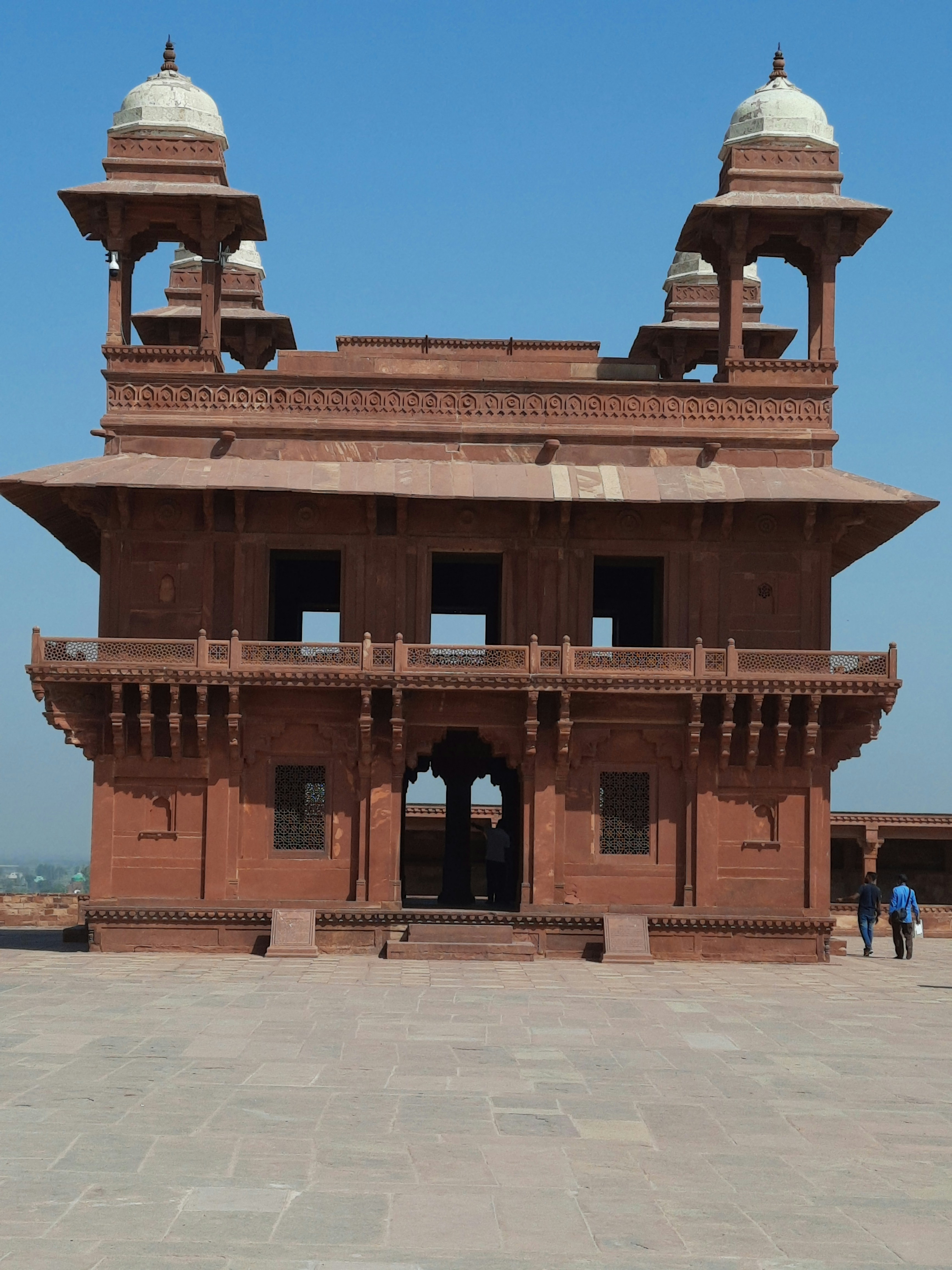 Historic red sandstone building with intricate carvings and domed towers against a clear blue sky.
