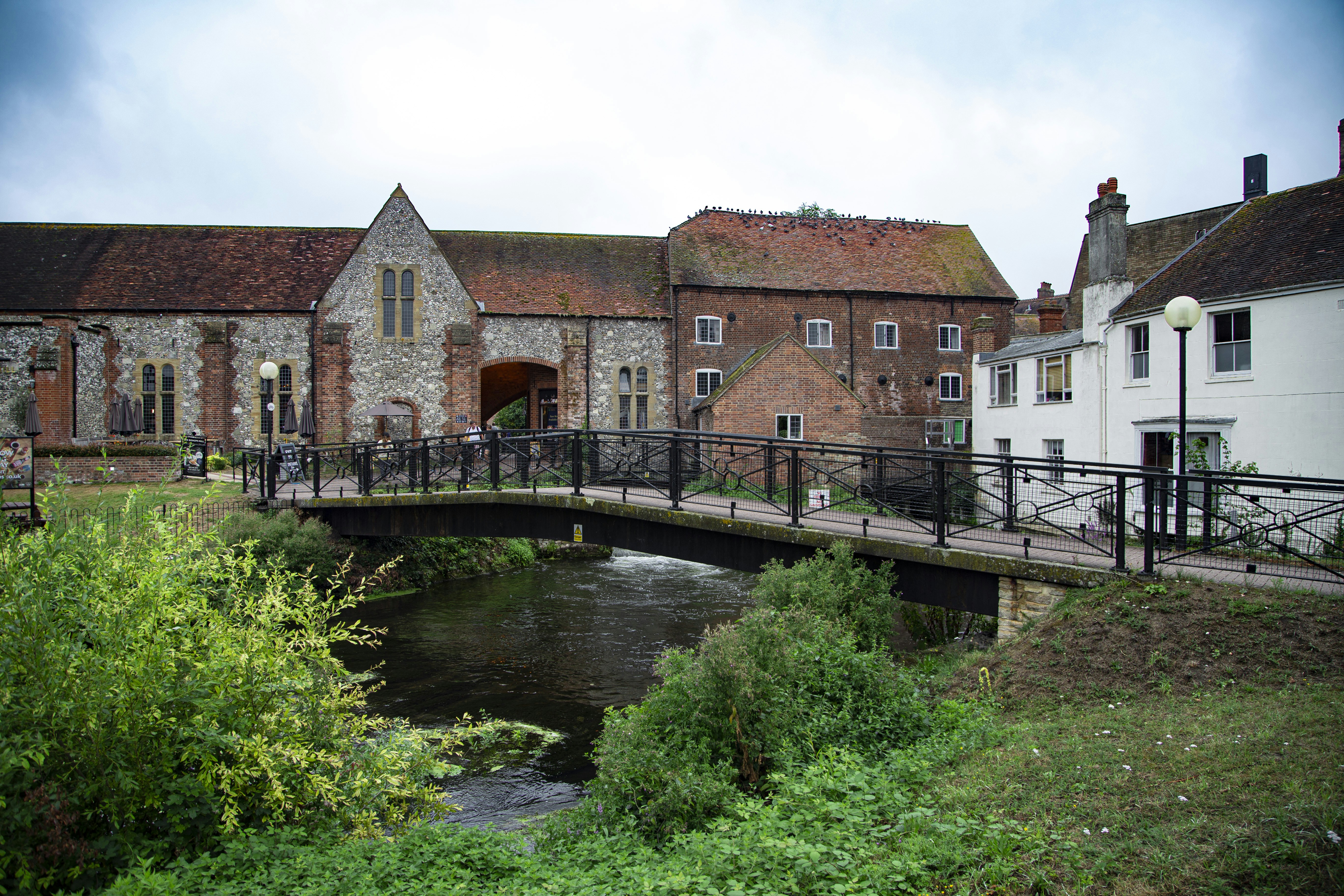 Charming stone buildings flanking a tranquil stream, with a bridge connecting the two sides. The scene reflects a blend of nature and architecture.