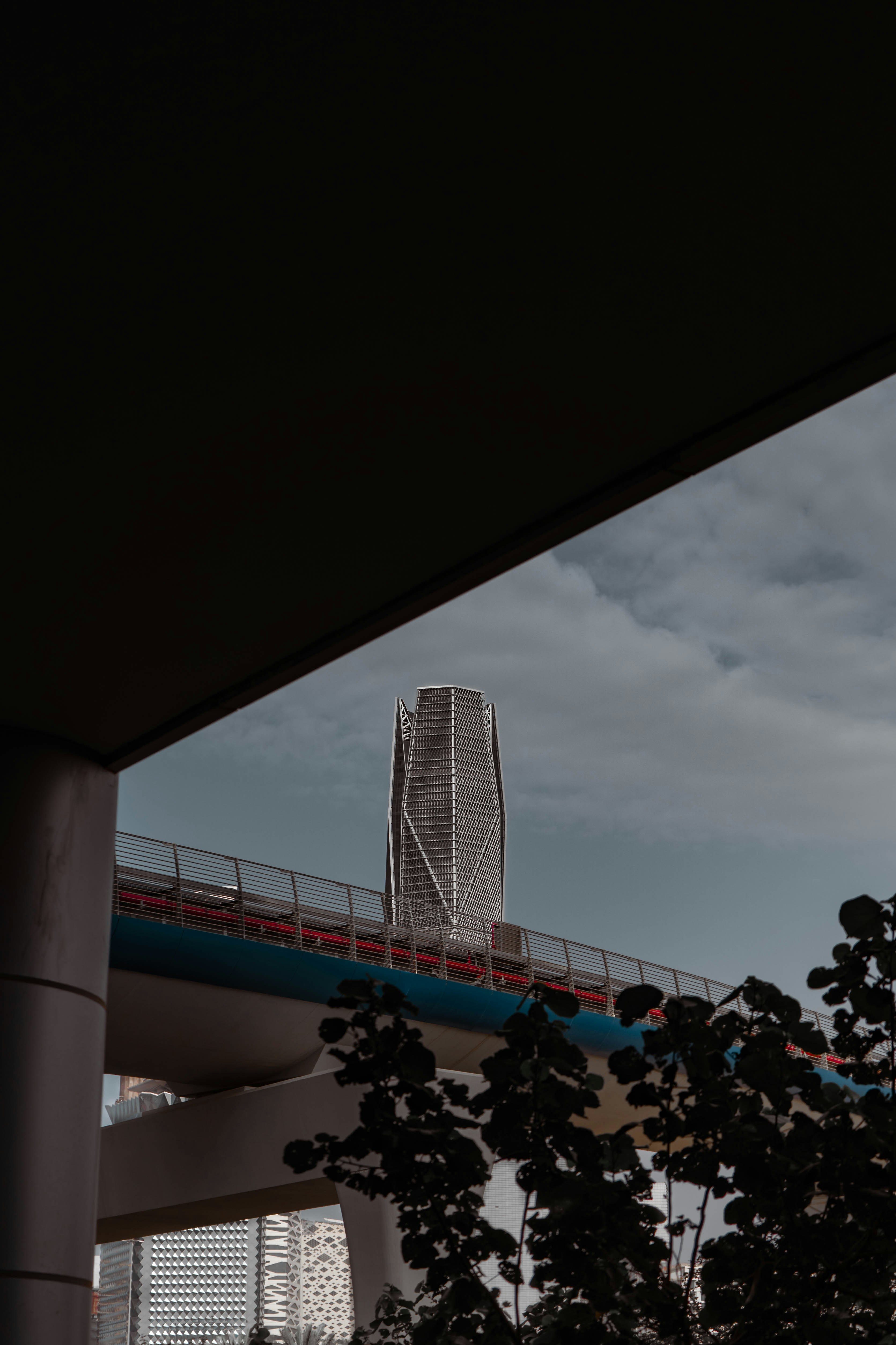 A sleek skyscraper rises above a modern overpass, framed by lush greenery and contrasting architectural lines. The scene captures the harmony between nature and urban development.