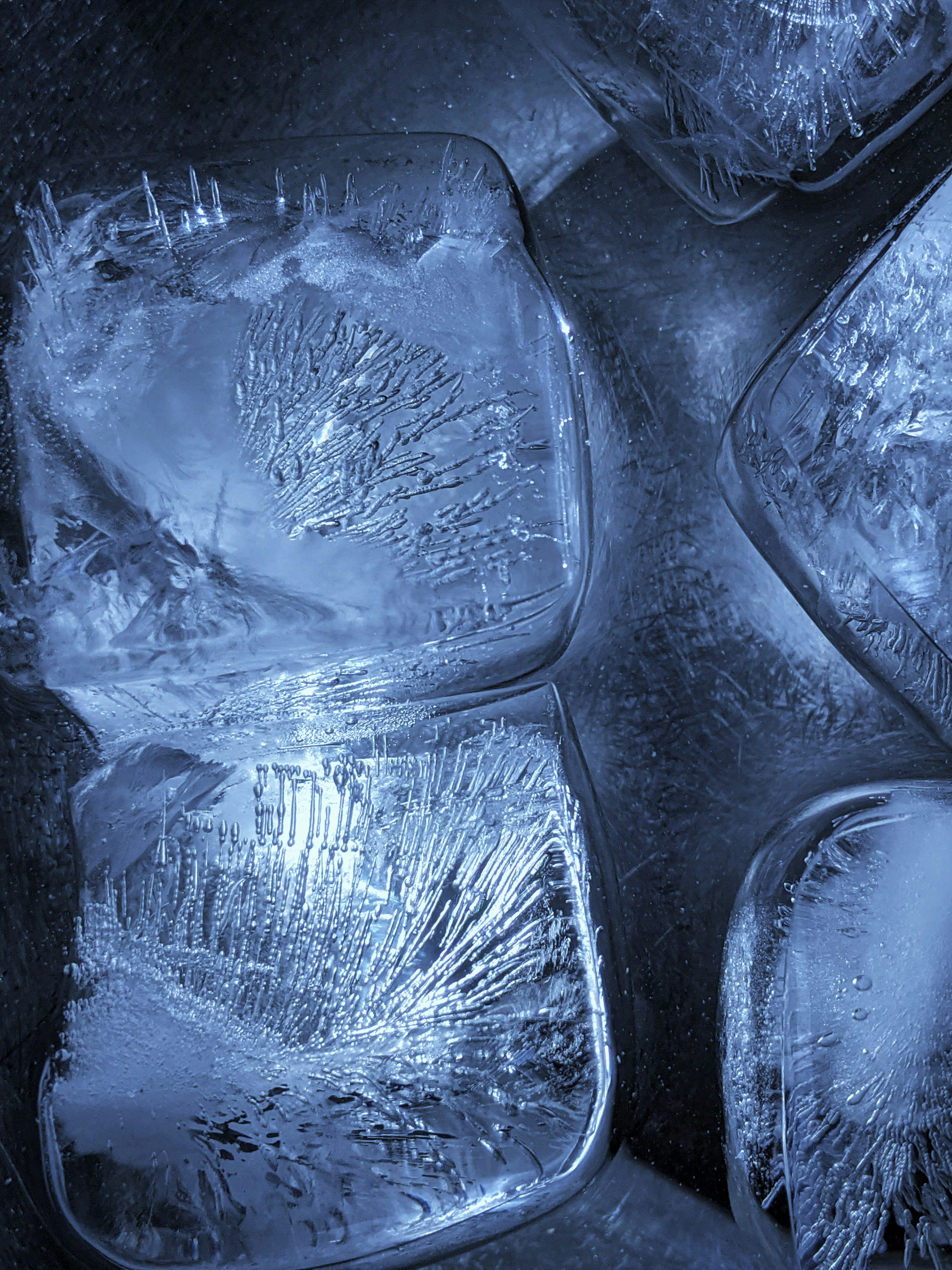 Close-up of ice cubes with intricate surface patterns reflecting light in a metallic container.