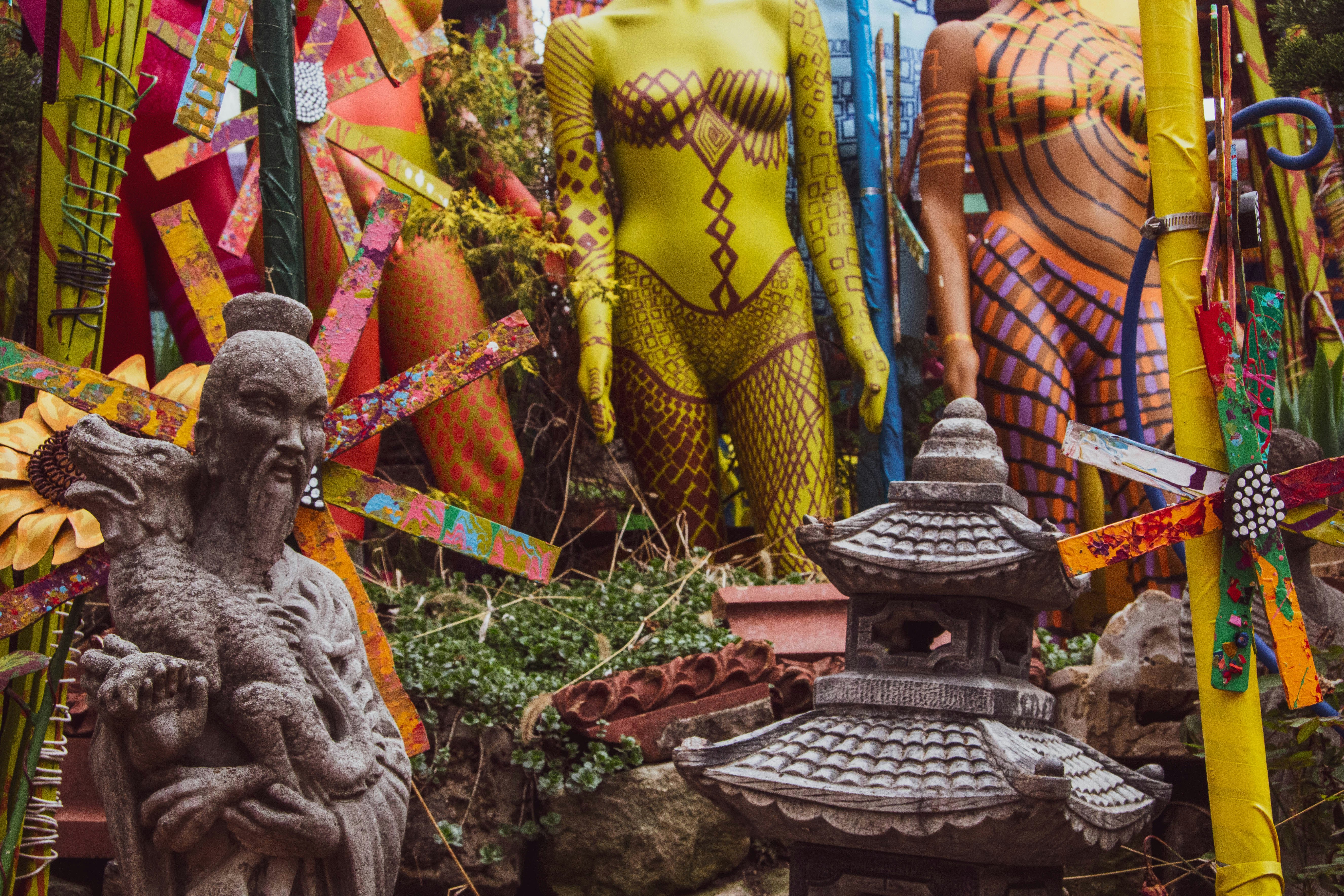 Colorful mannequins adorned with intricate patterns stand amidst traditional sculptures in a lively outdoor display. A blend of modern and historical art forms creates a unique visual narrative.