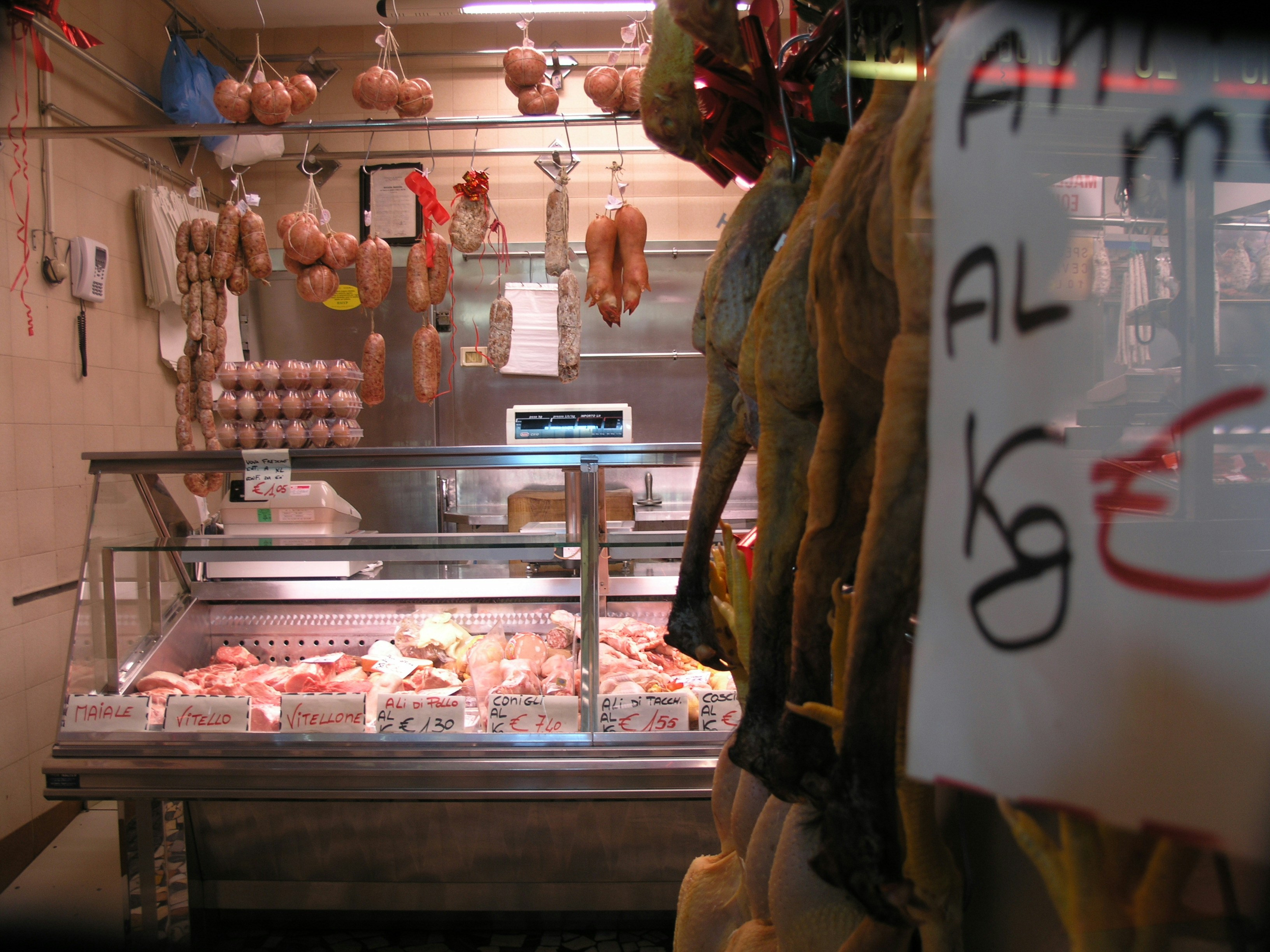 A bustling butcher shop displaying an array of meats and sausages, with a prominent glass display case showcasing fresh cuts. The atmosphere is vibrant and inviting.