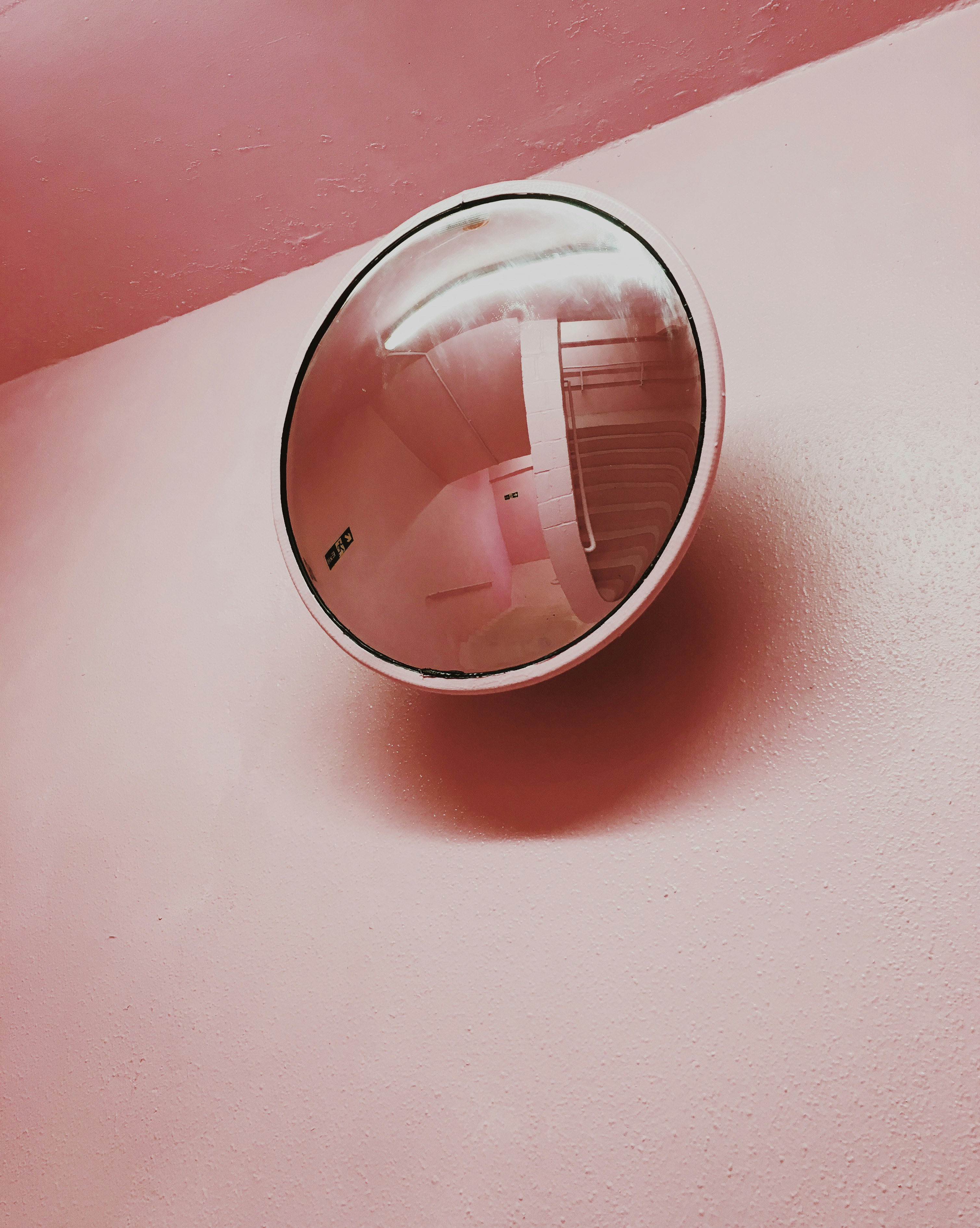 Curved mirror reflecting a soft pink wall, creating an intriguing visual interplay of colors and shapes.