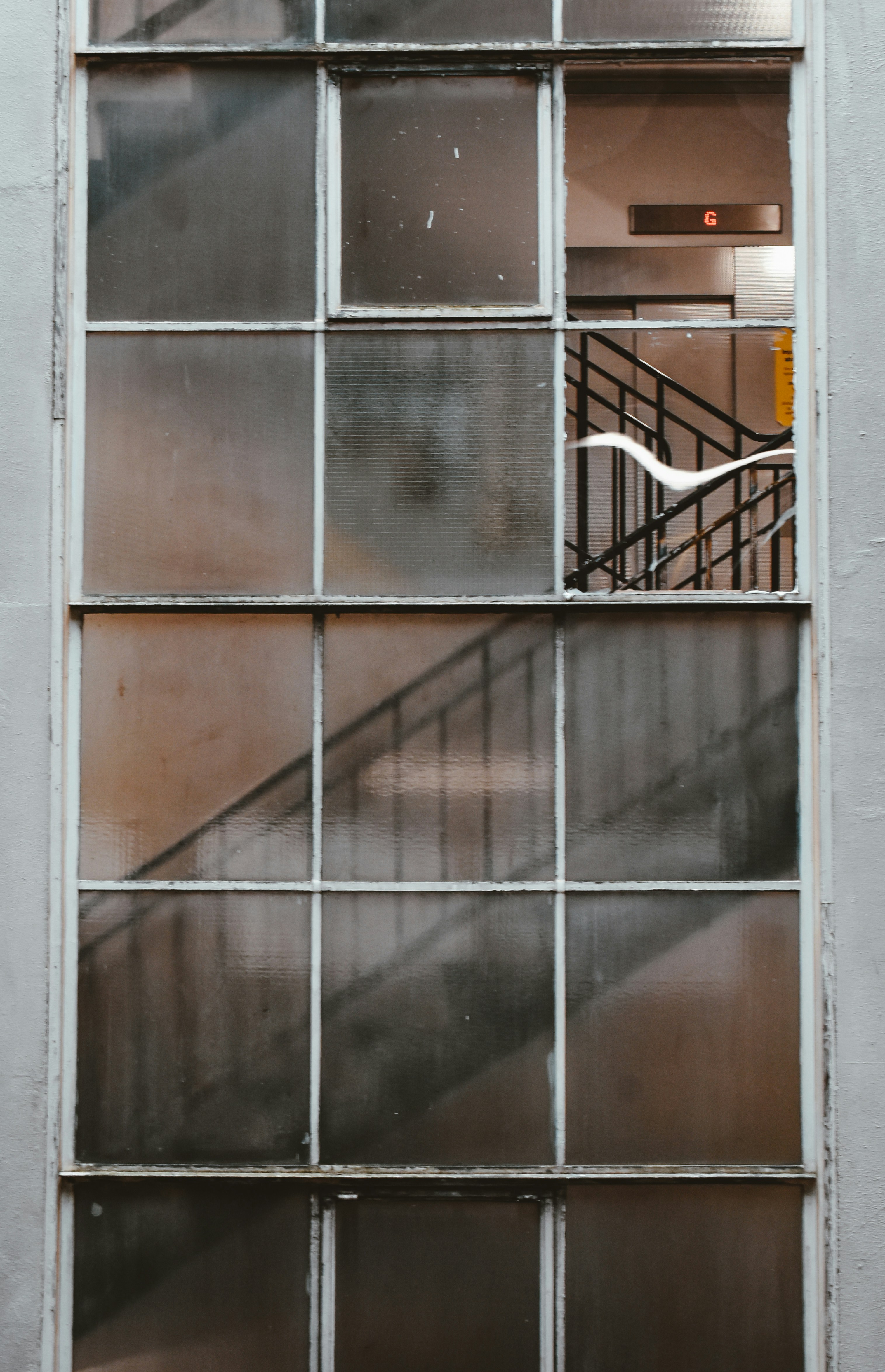 Translucent windowpanes frame a staircase, revealing the interplay of light and shadow within a building's interior.