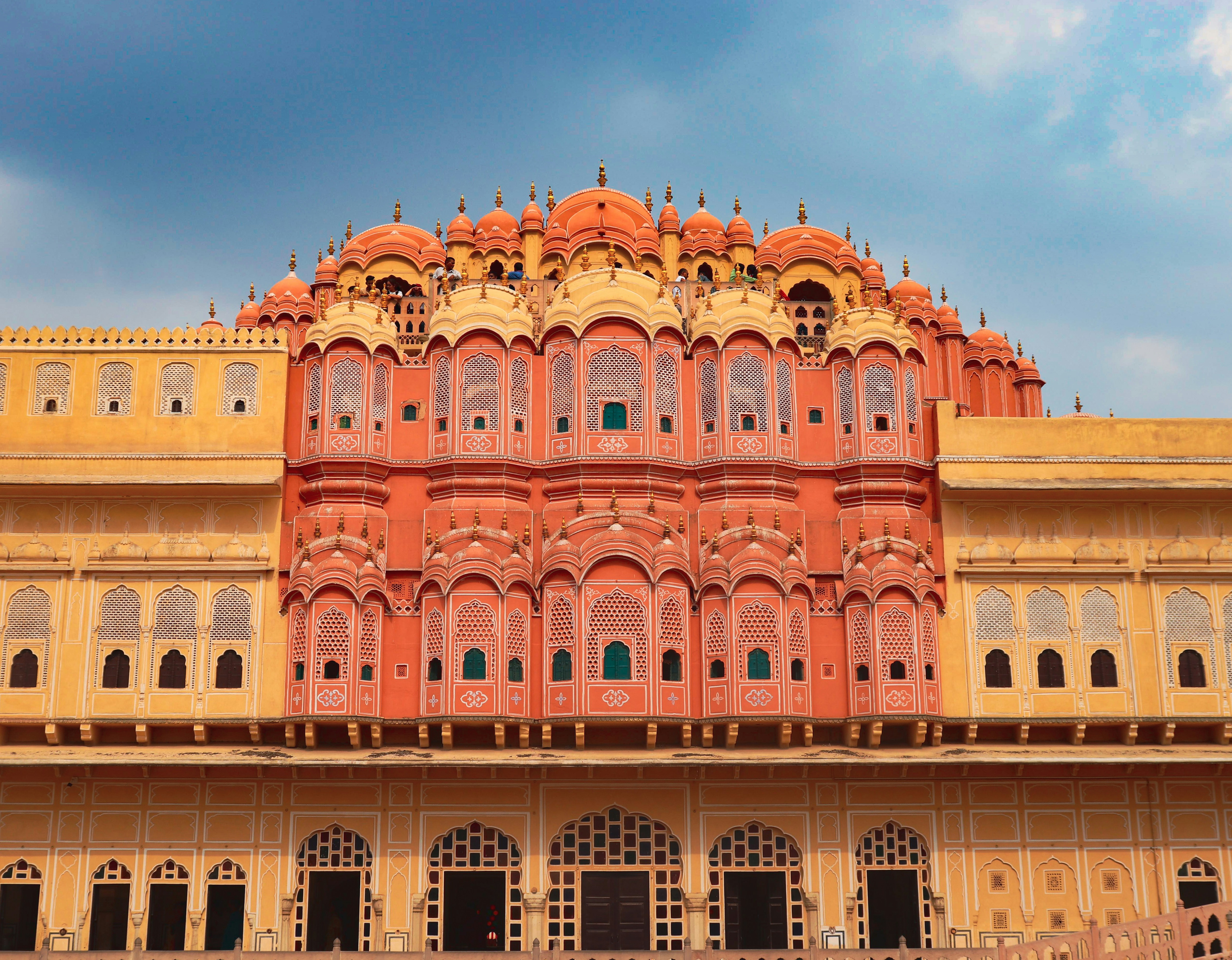Intricate architectural details of the Hawa Mahal in Jaipur, showcasing its vibrant pink and yellow hues under a dramatic sky.
