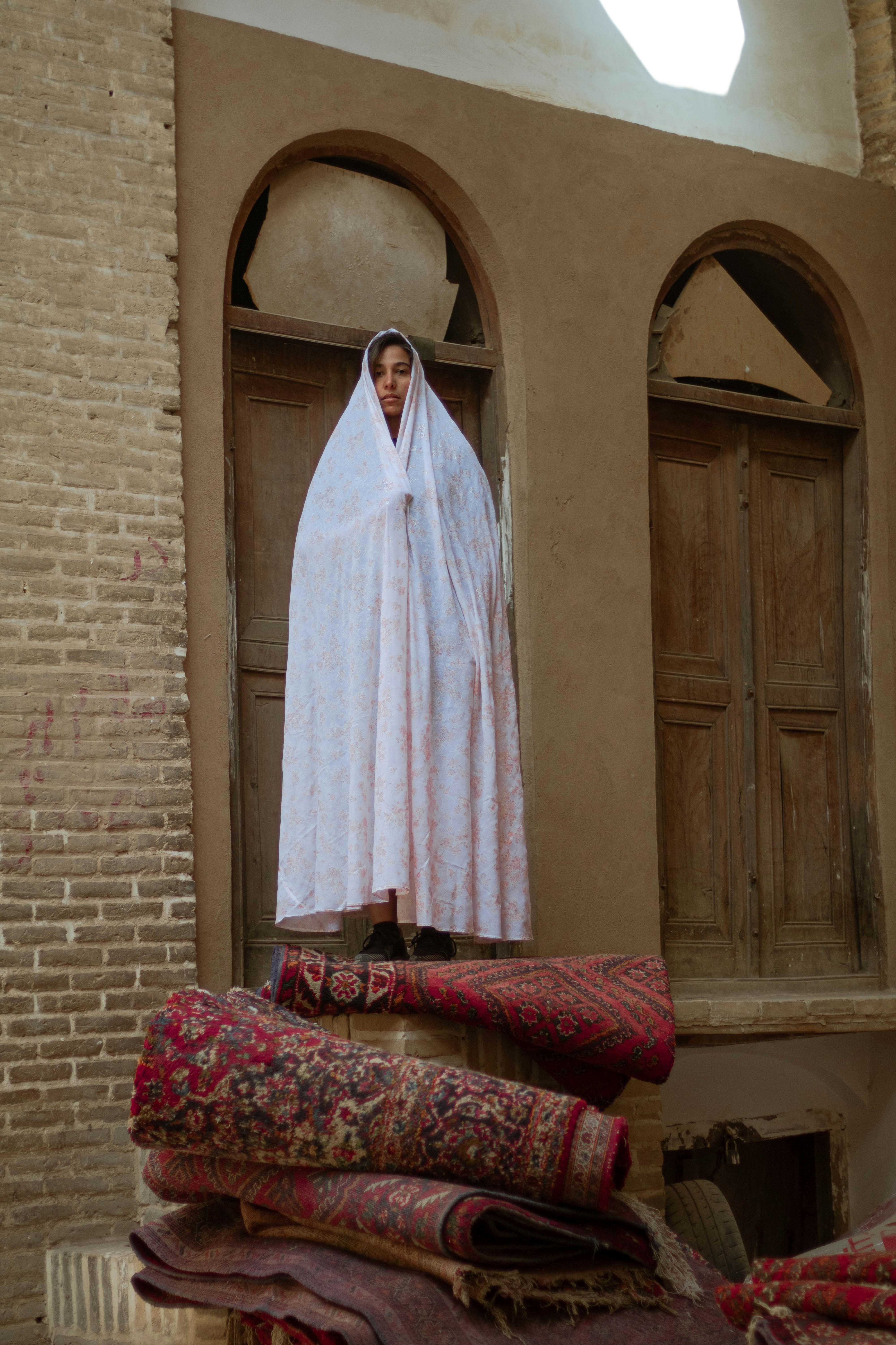 White-wrapped silhouette on a rug pedestal beneath sunlit arches