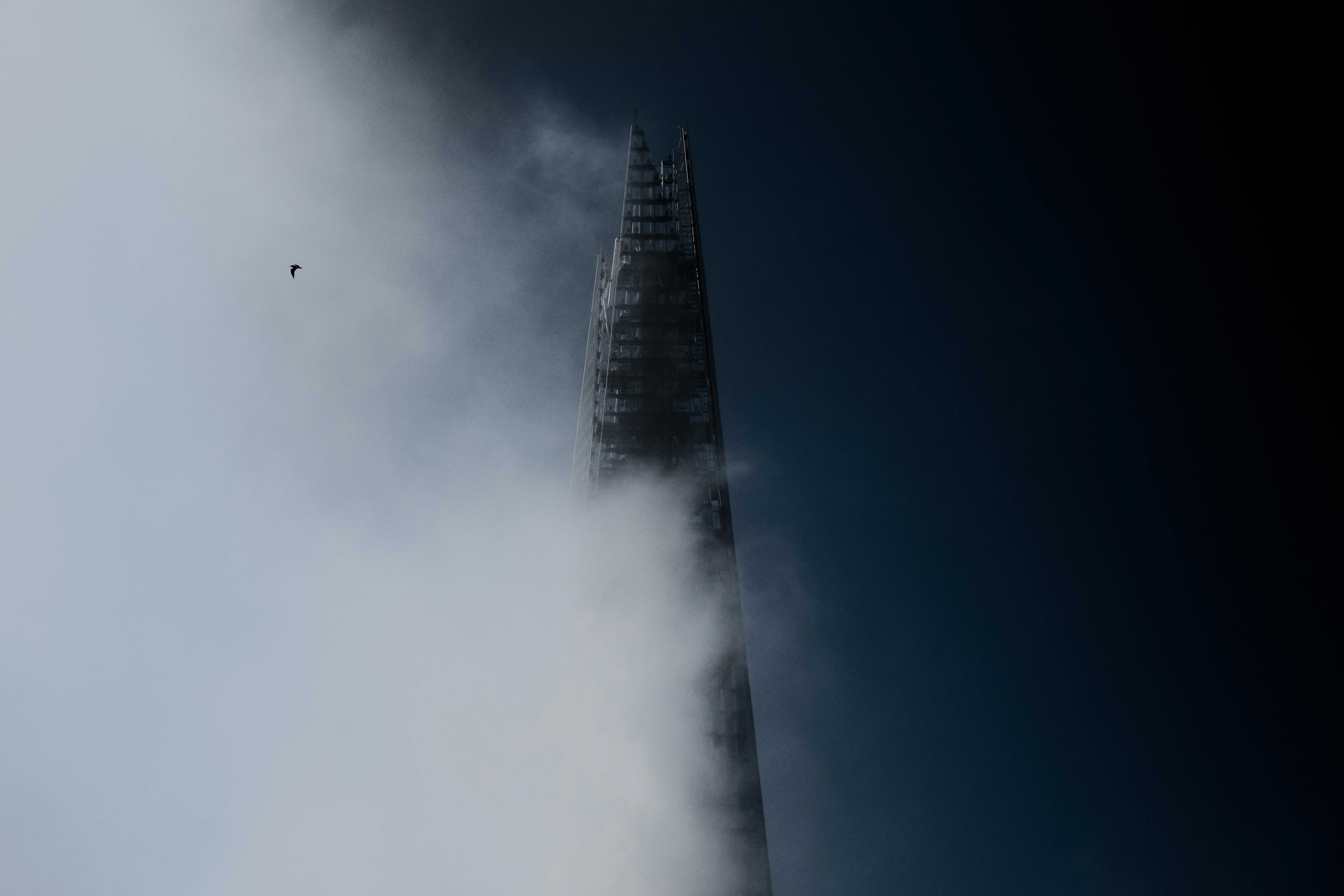 A towering structure piercing through a veil of fog against a dark sky, evoking a sense of mystery and grandeur.