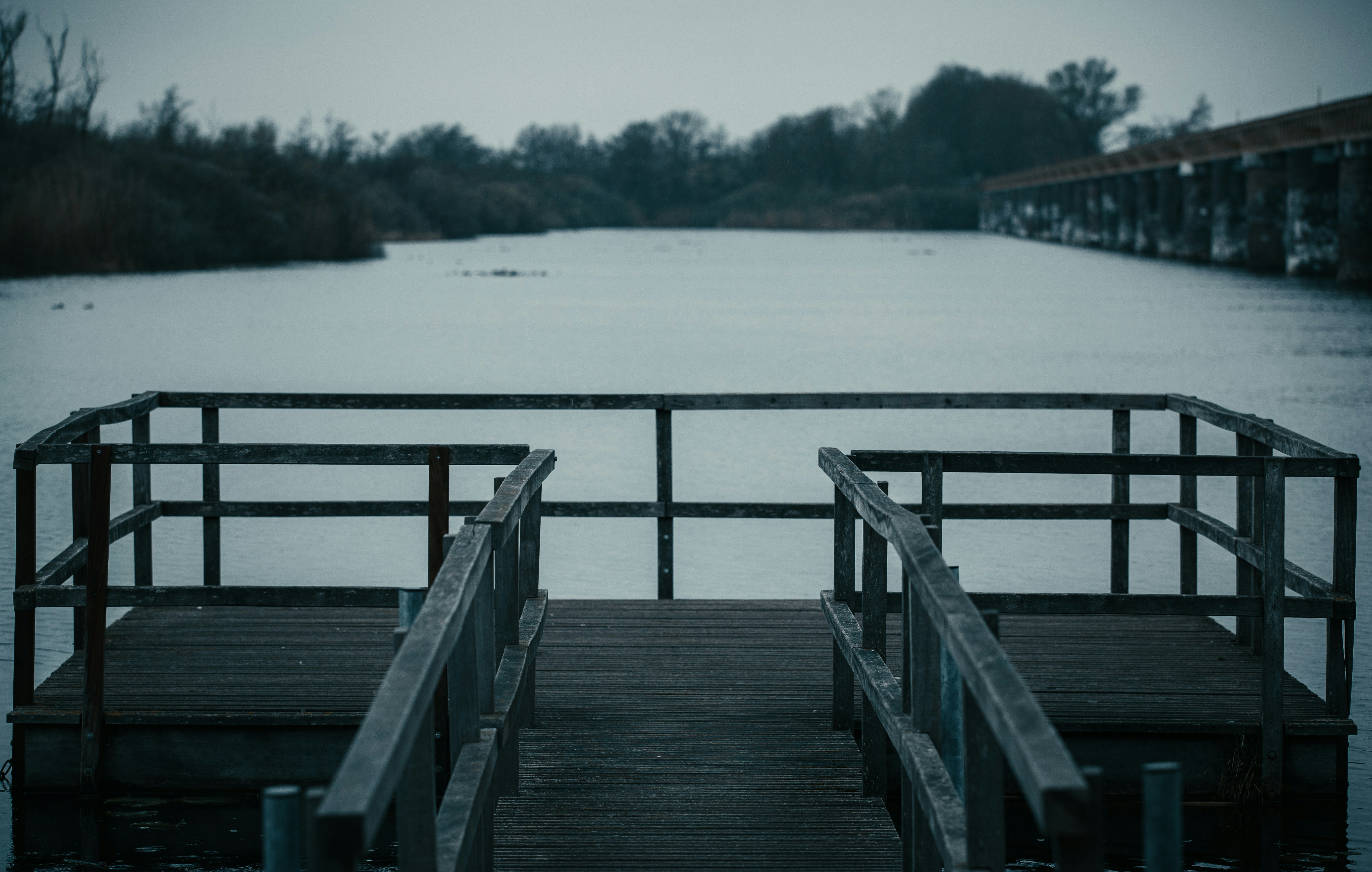 Weathered dock extending into a calm, misty waterway, surrounded by muted foliage. The scene evokes a sense of tranquility and reflection.