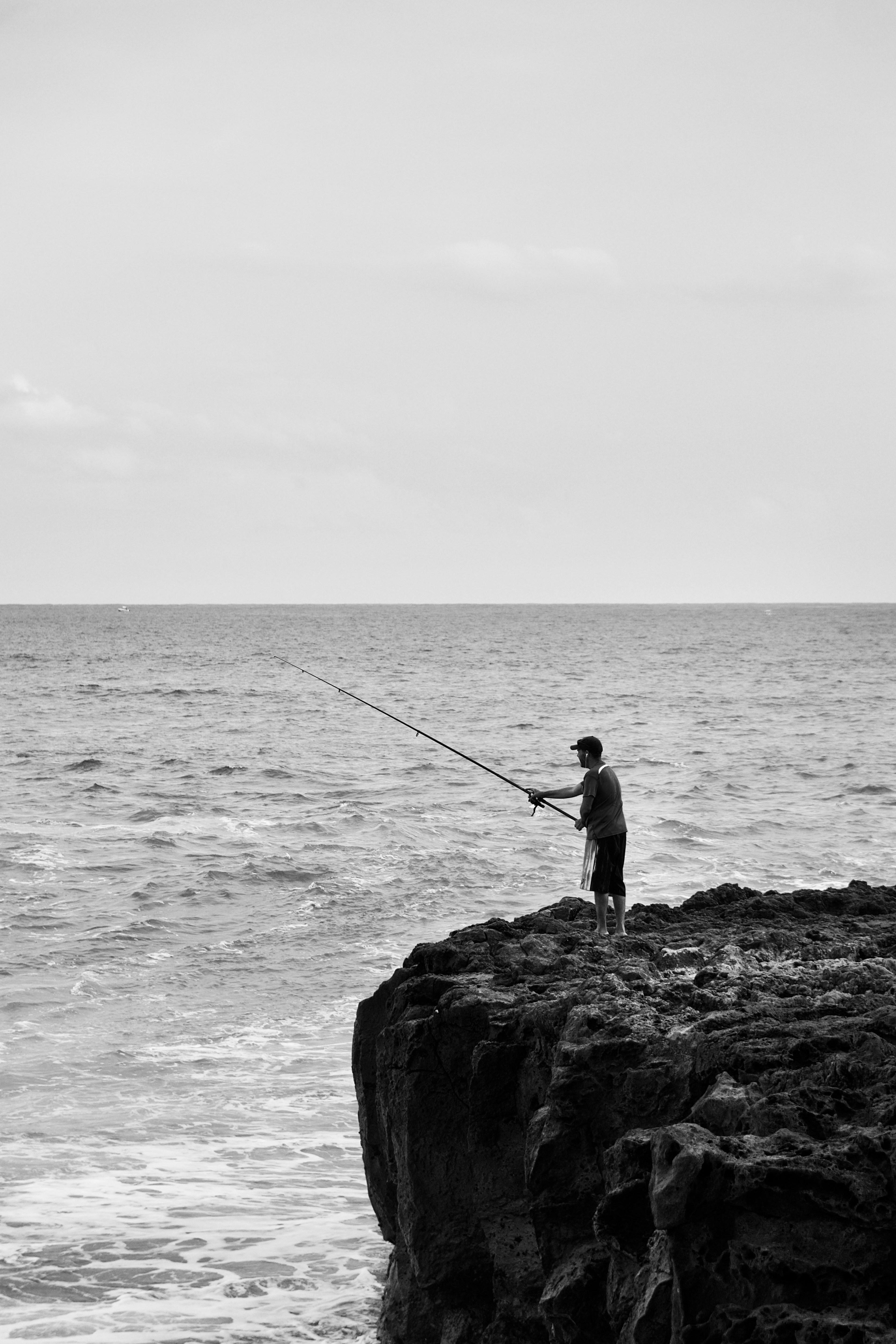 Man fishing on a rocky cliff overlooking the ocean.