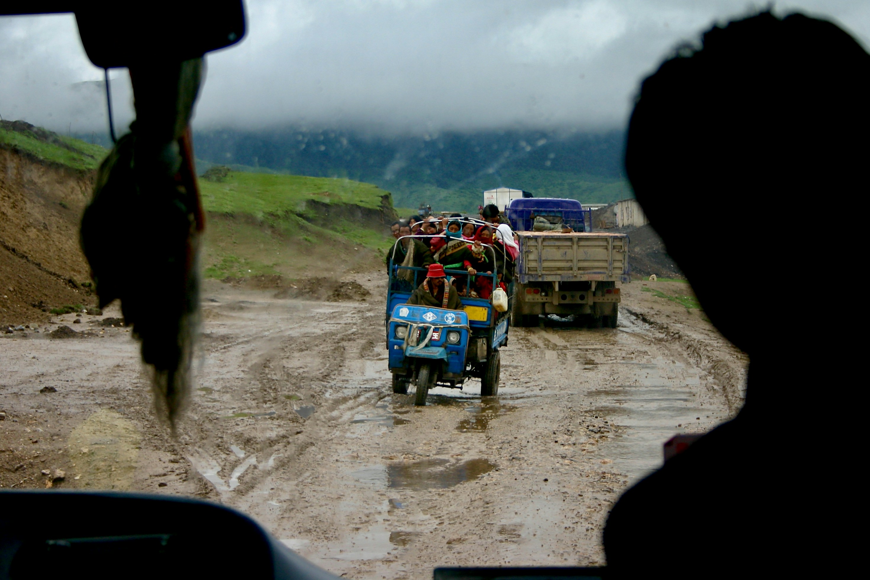Mud-Splashed Convoy: A Blue Jeep Navigates a Rain-Washed Rural Track