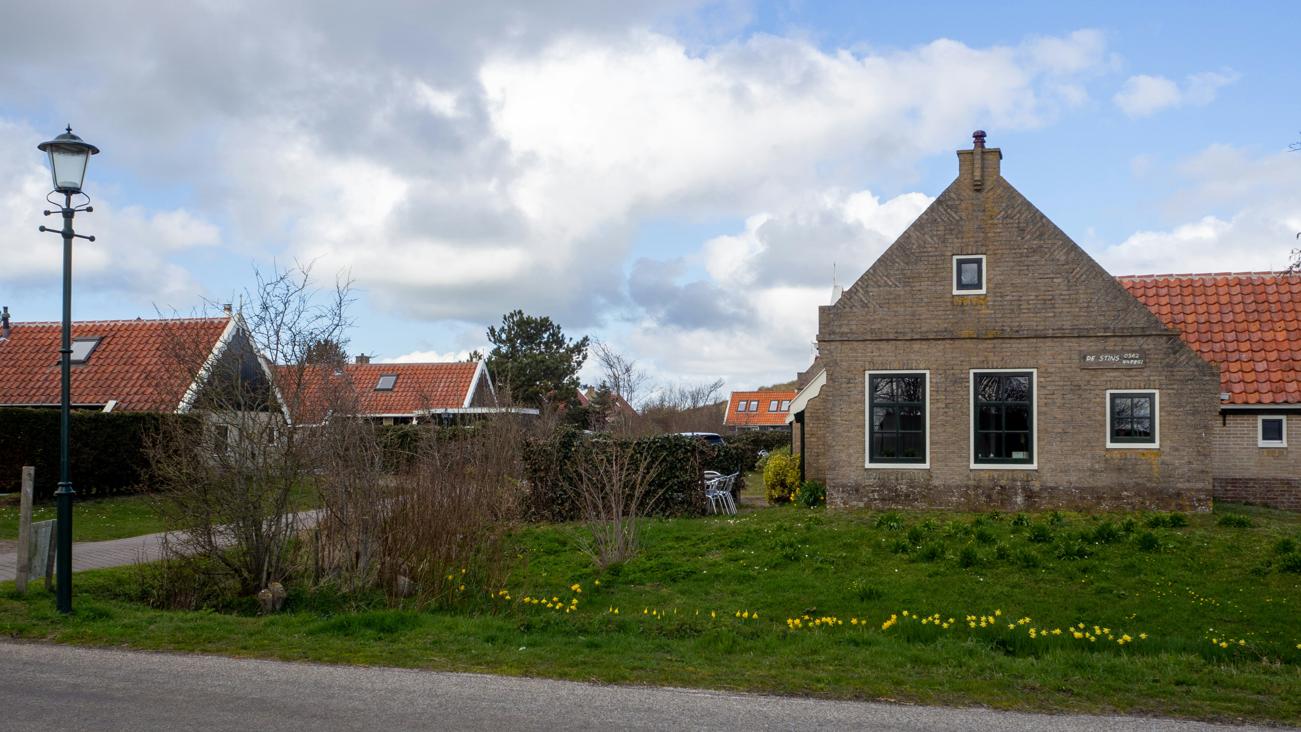 Traditional Dutch house framed by blooming daffodils and rustic street lamp, set against a backdrop of cloudy skies.
