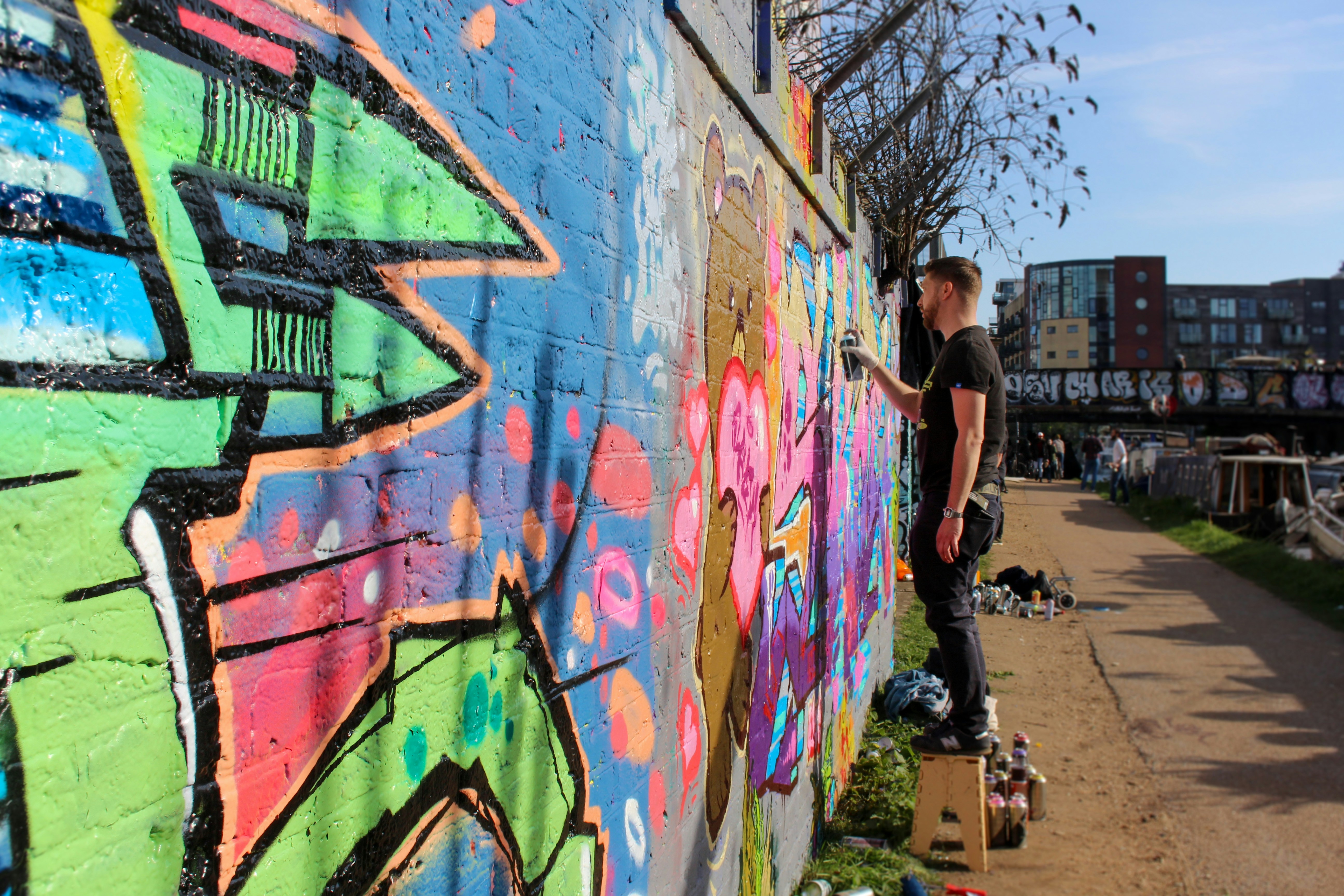 Spray and Spectrum: A muralist colors a sunlit urban brick wall